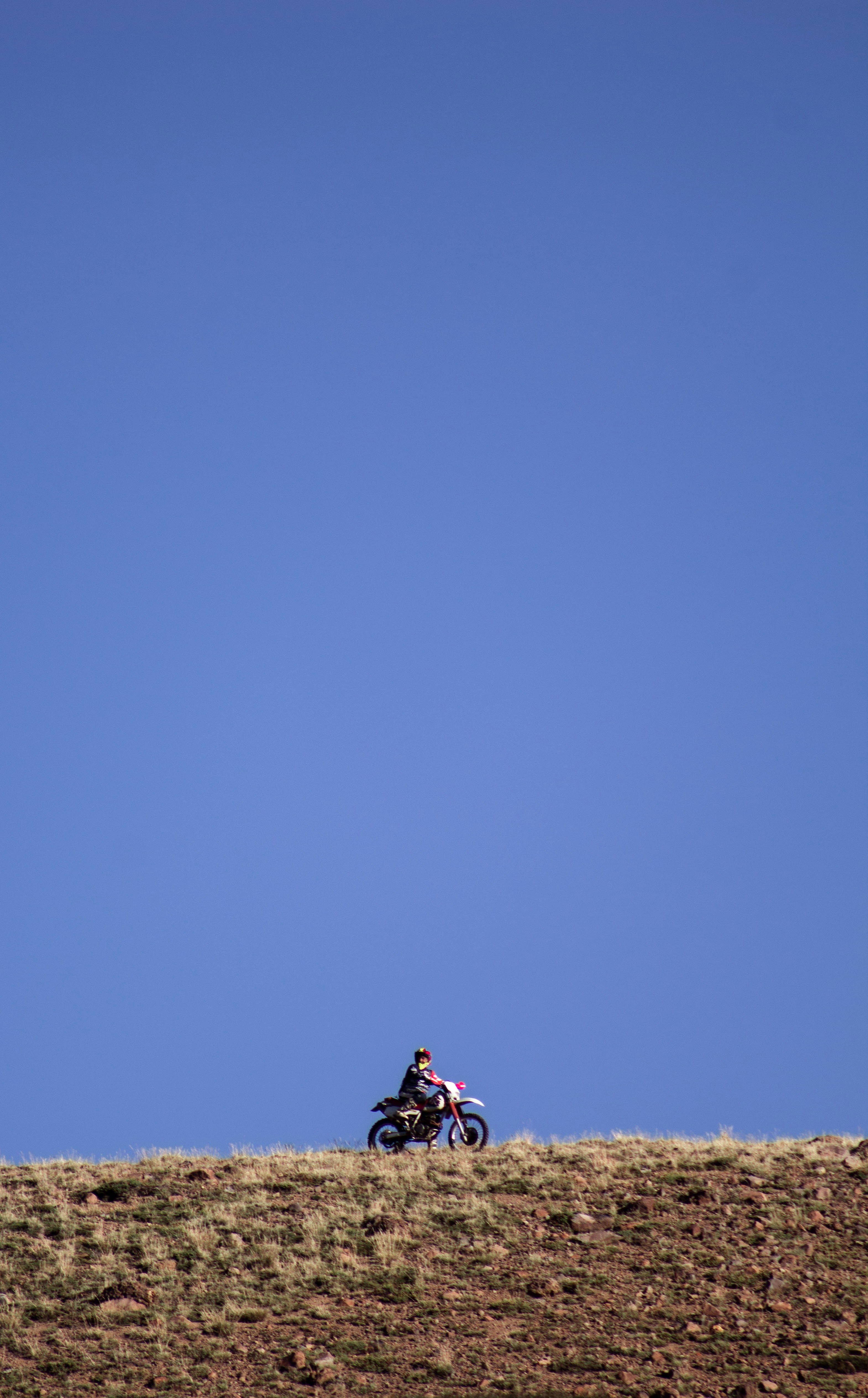 A motorcyclist navigating a rugged terrain under a clear blue sky, showcasing the thrill of off-road riding.