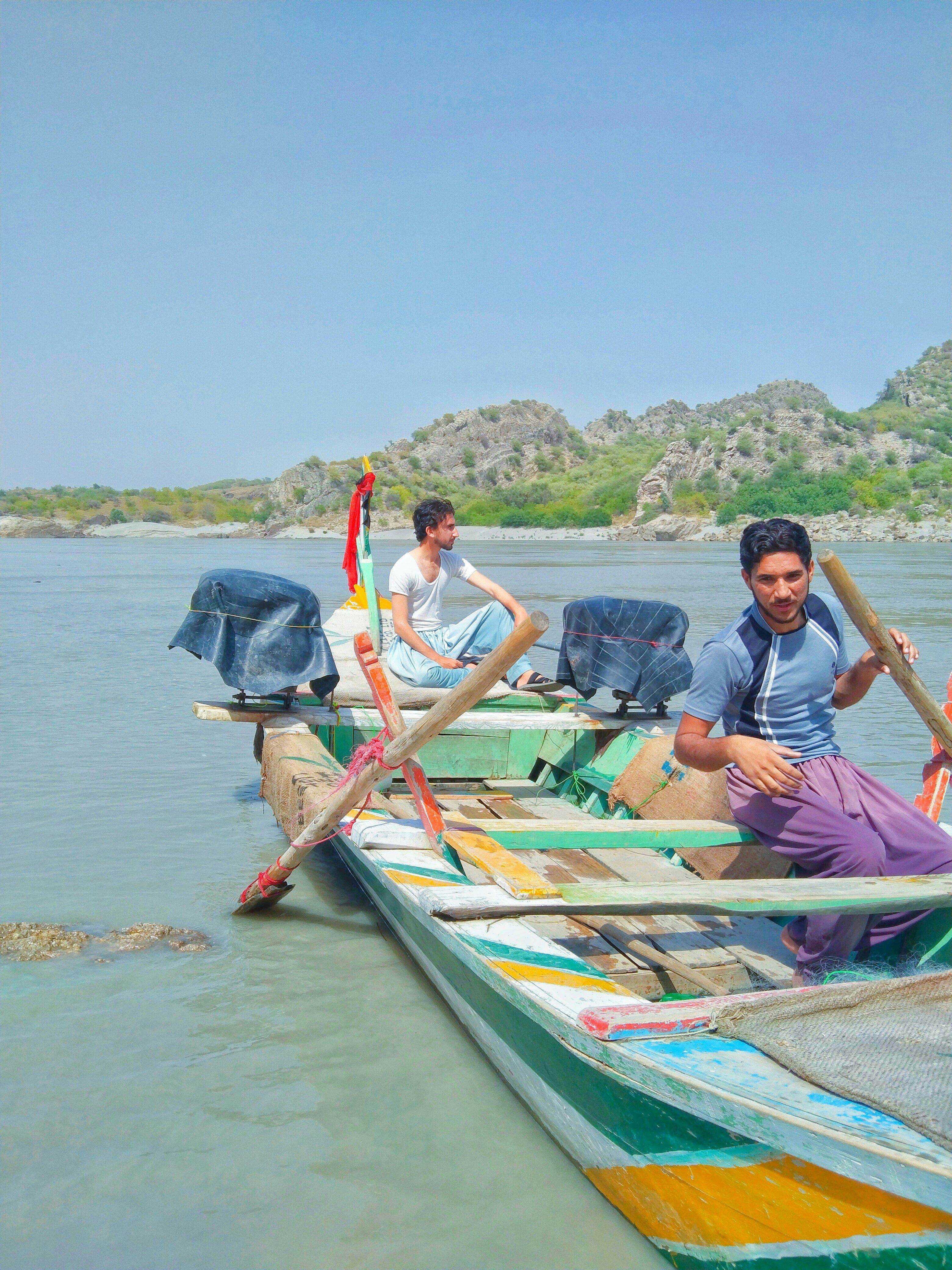 Two Oarsmen on a Vibrant Boat Against Turquoise Coastal Waters