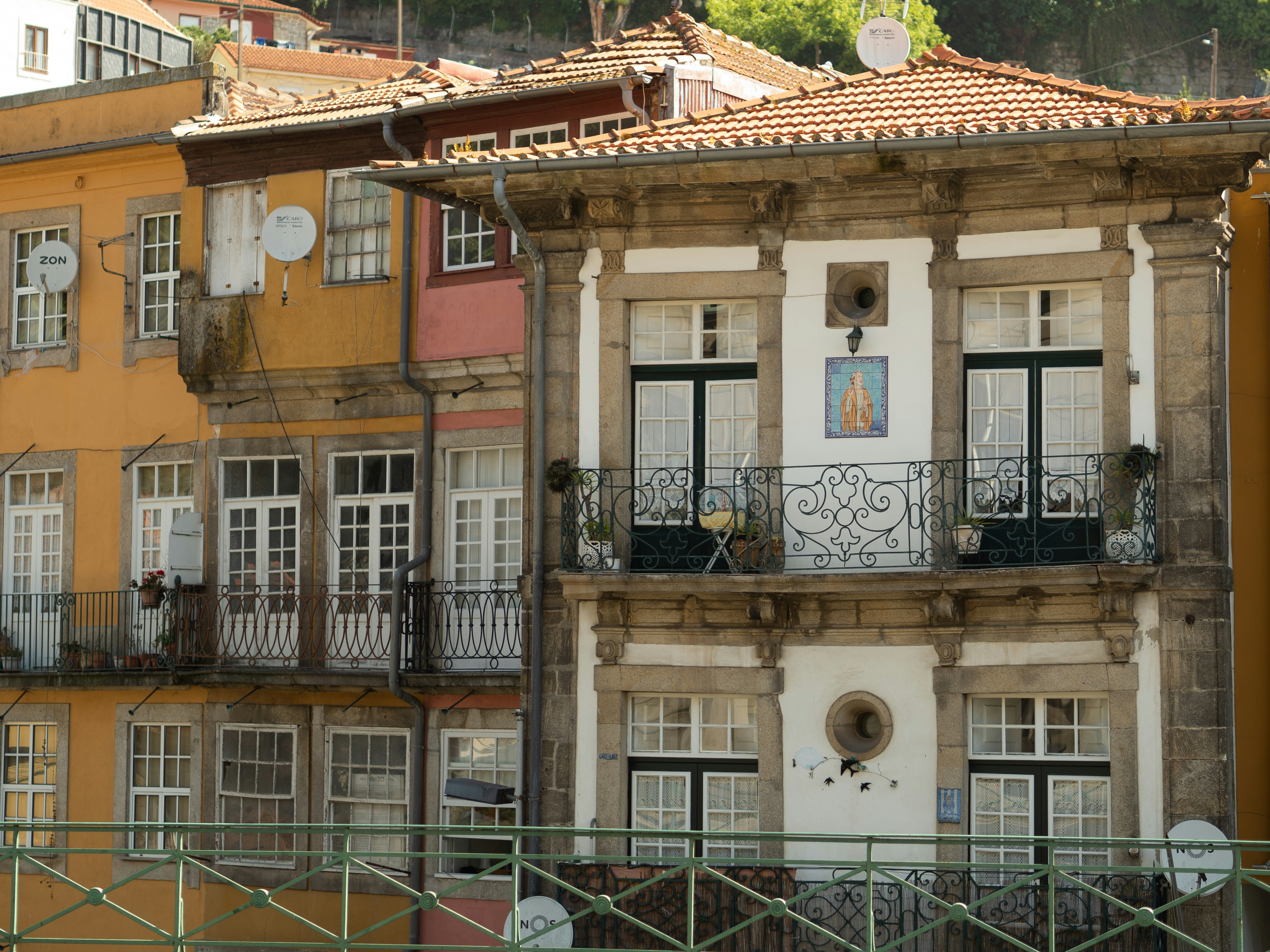 Colorful buildings with intricate balconies and satellite dishes line a street in Porto, showcasing urban life and architectural diversity.