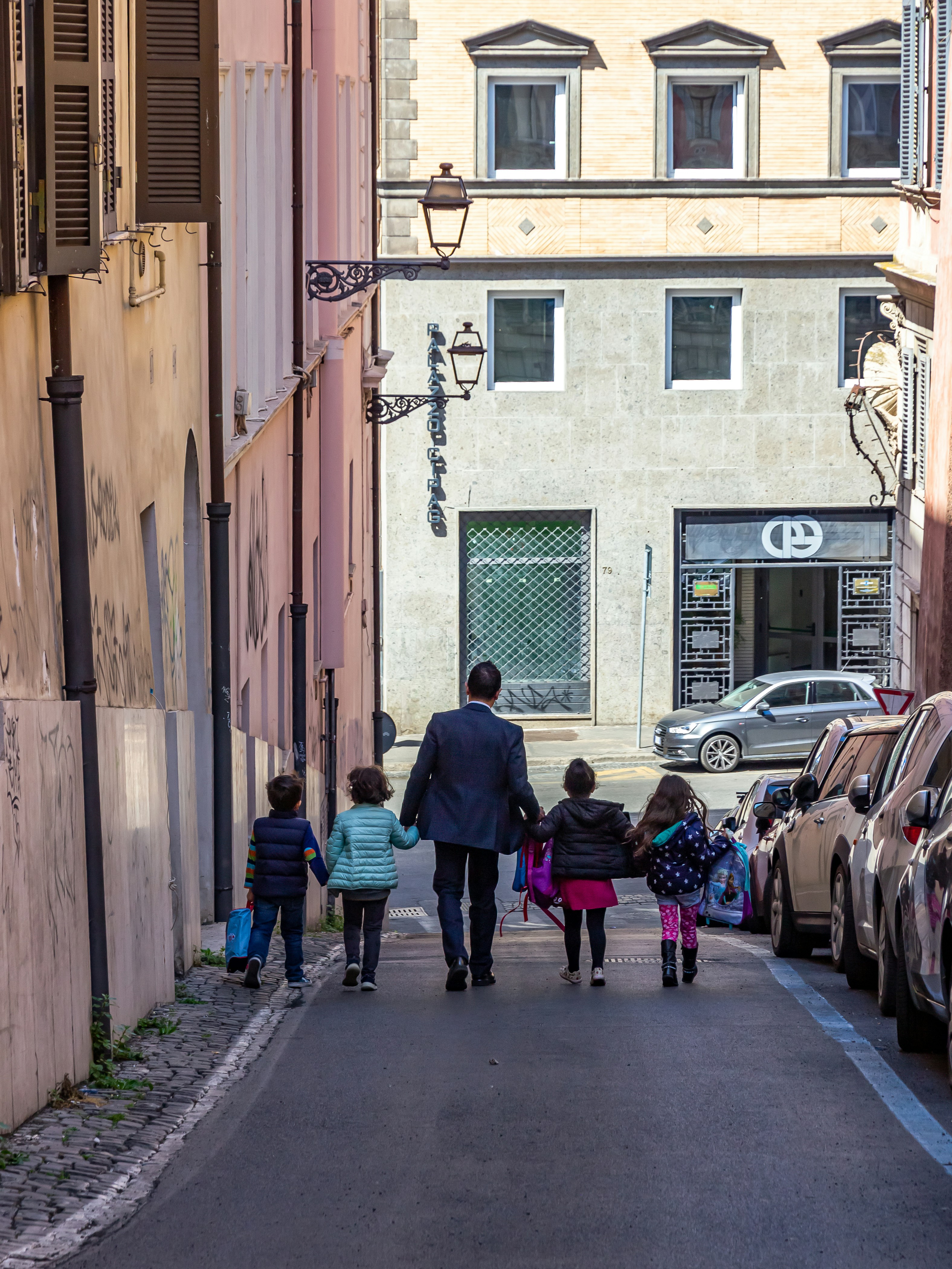 Sunlit Alleyway: A Father Leads Children Through a Quiet European Street