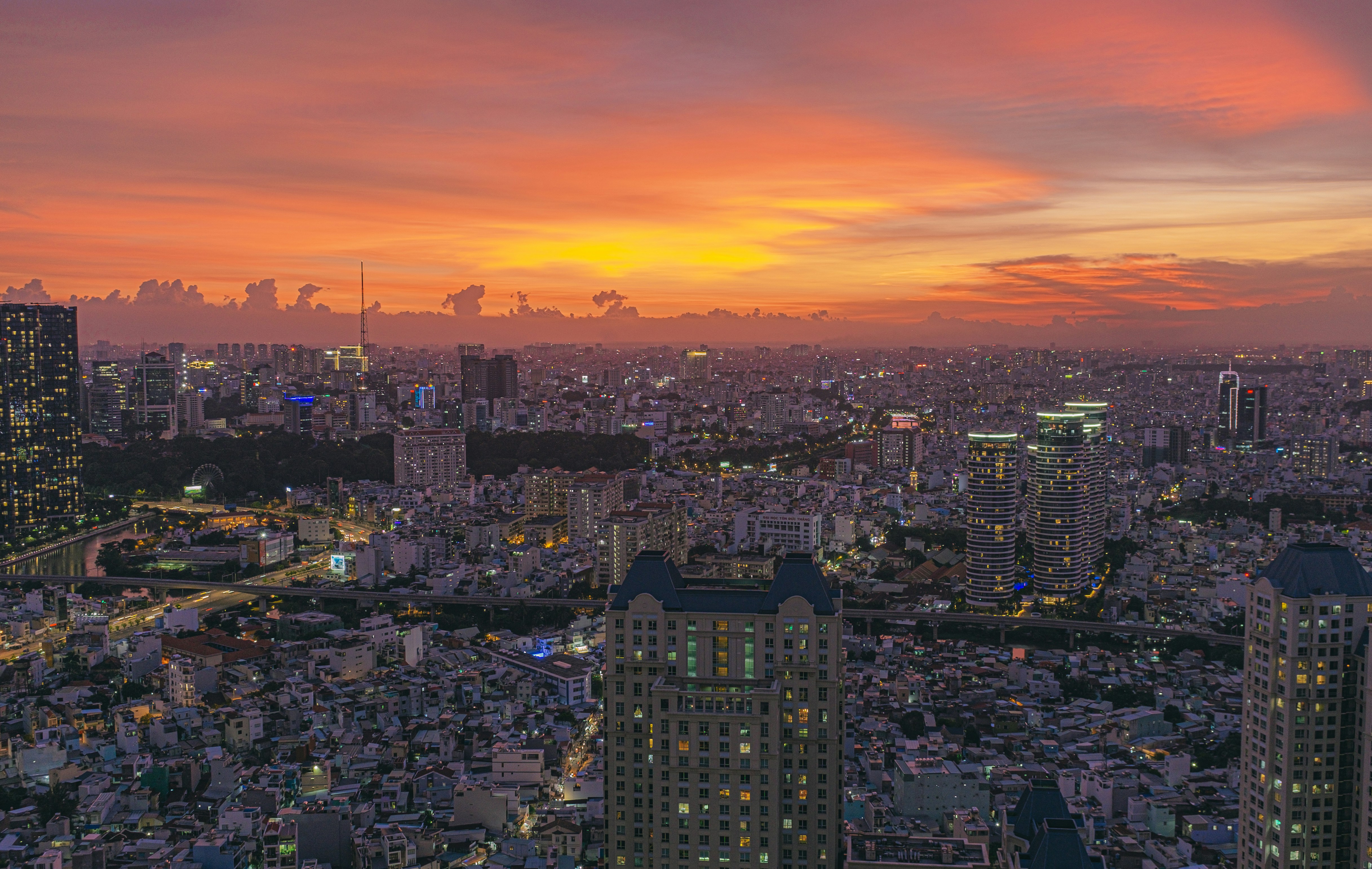 Vibrant sunset casts a warm glow over a sprawling cityscape, highlighting the contrast between modern skyscrapers and the intricate layout of urban life.