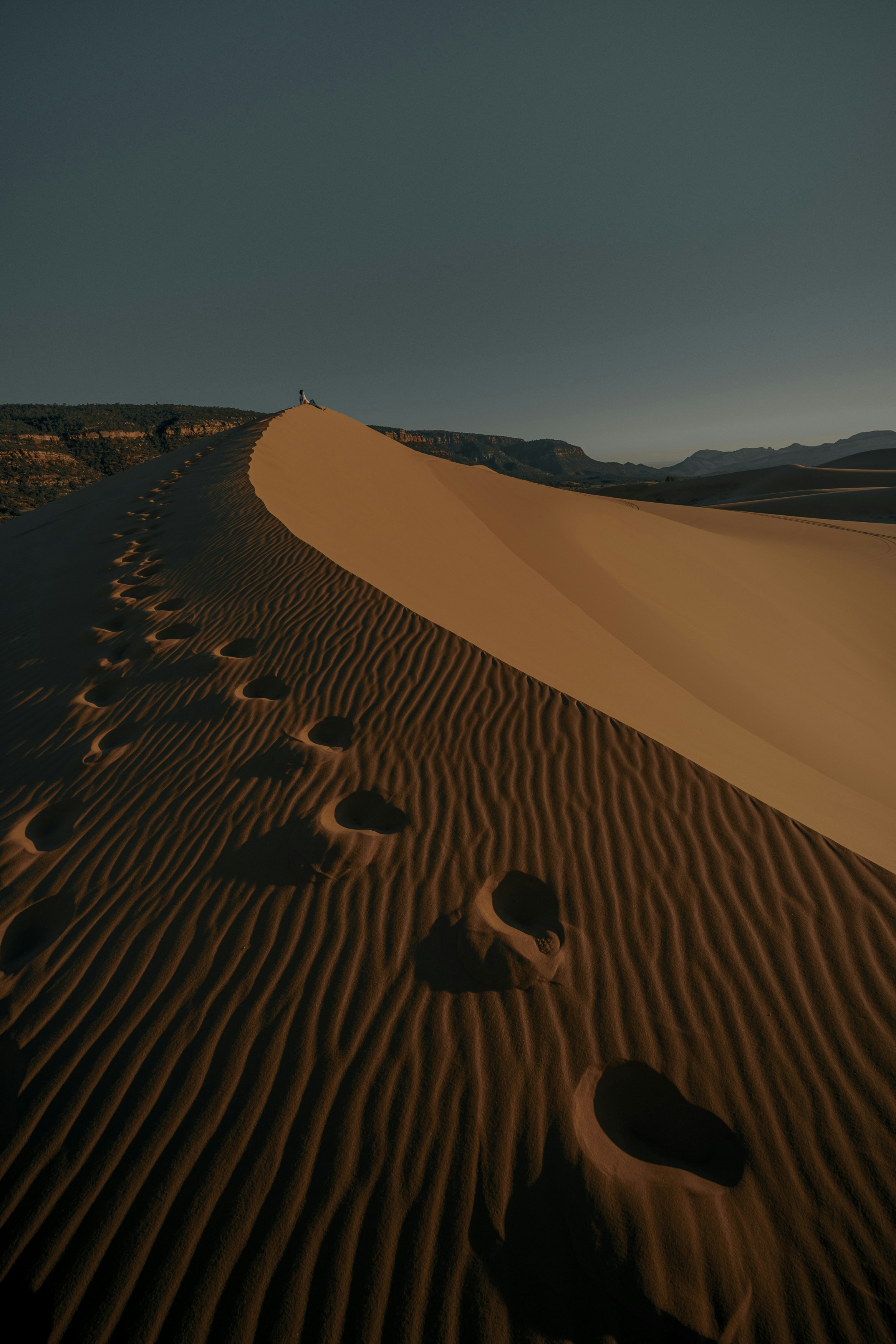 Footprints toward the Crest: A Solitary Figure Climbs a Sun-Warmed Dune at Twilight