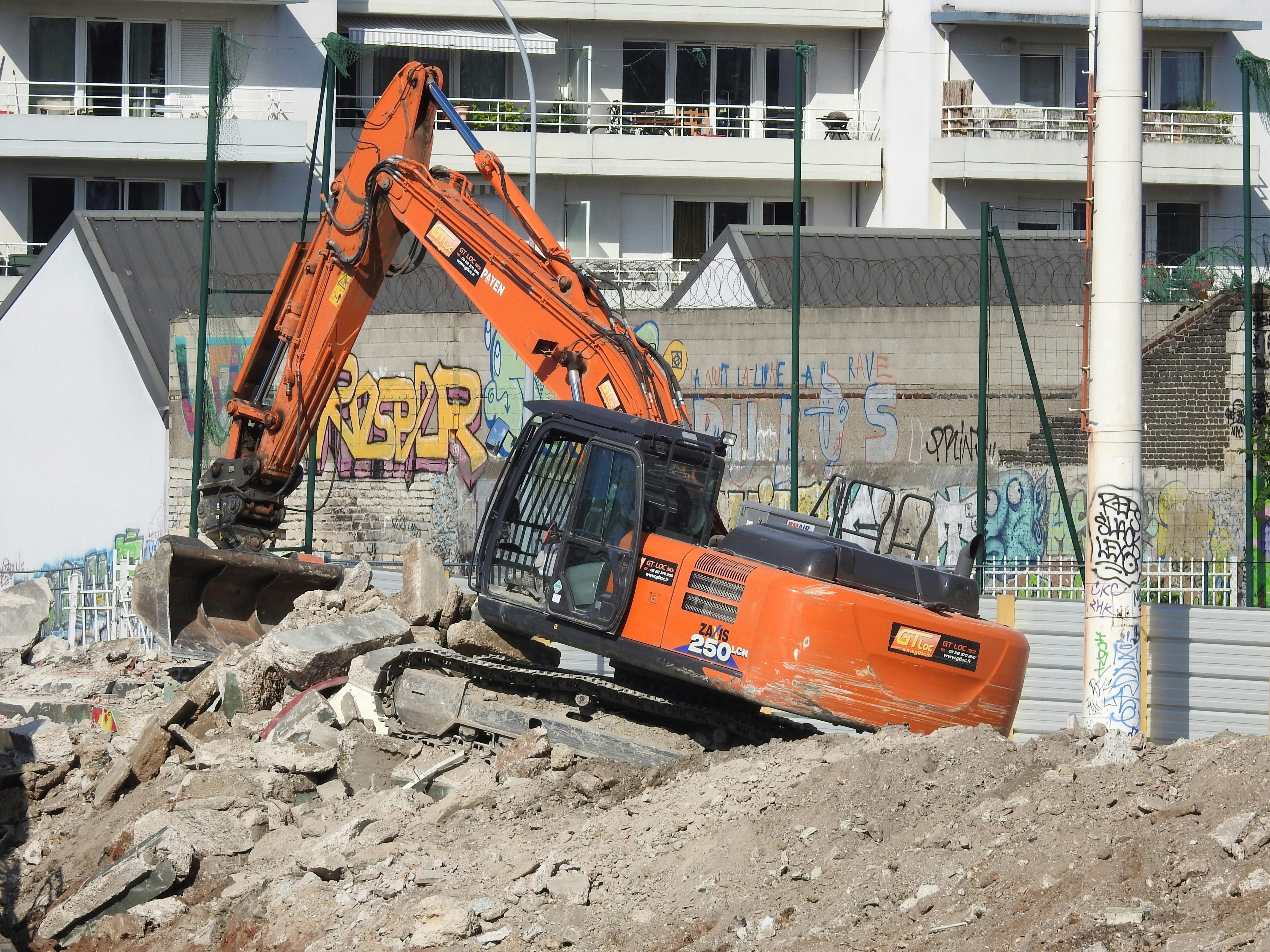 An orange excavator digging through a pile of rubble photo – Free ...