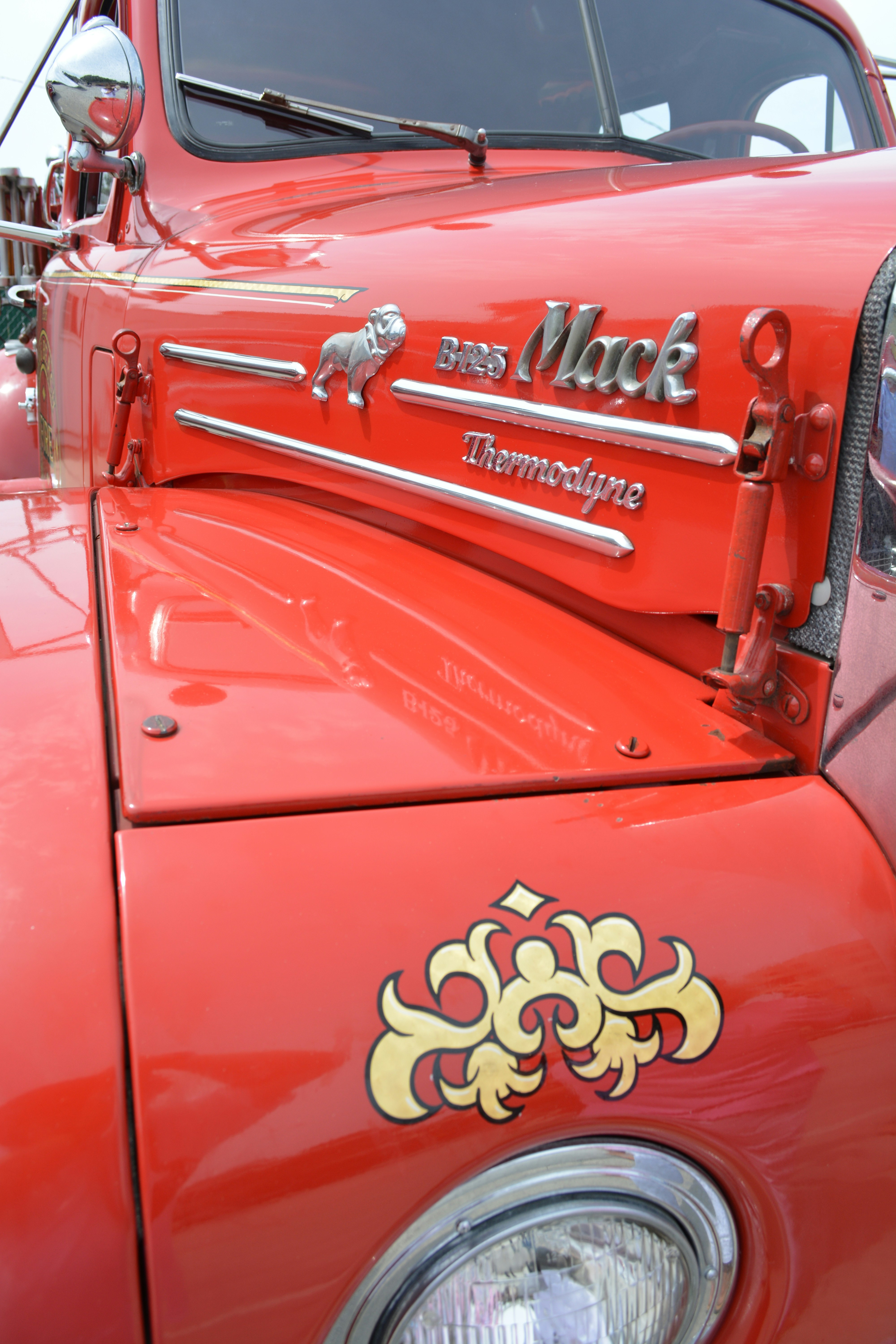 Close-up of a classic red Mack truck showcasing its iconic logo and detailed ornamentation on the hood. The design reflects a rich history of craftsmanship.