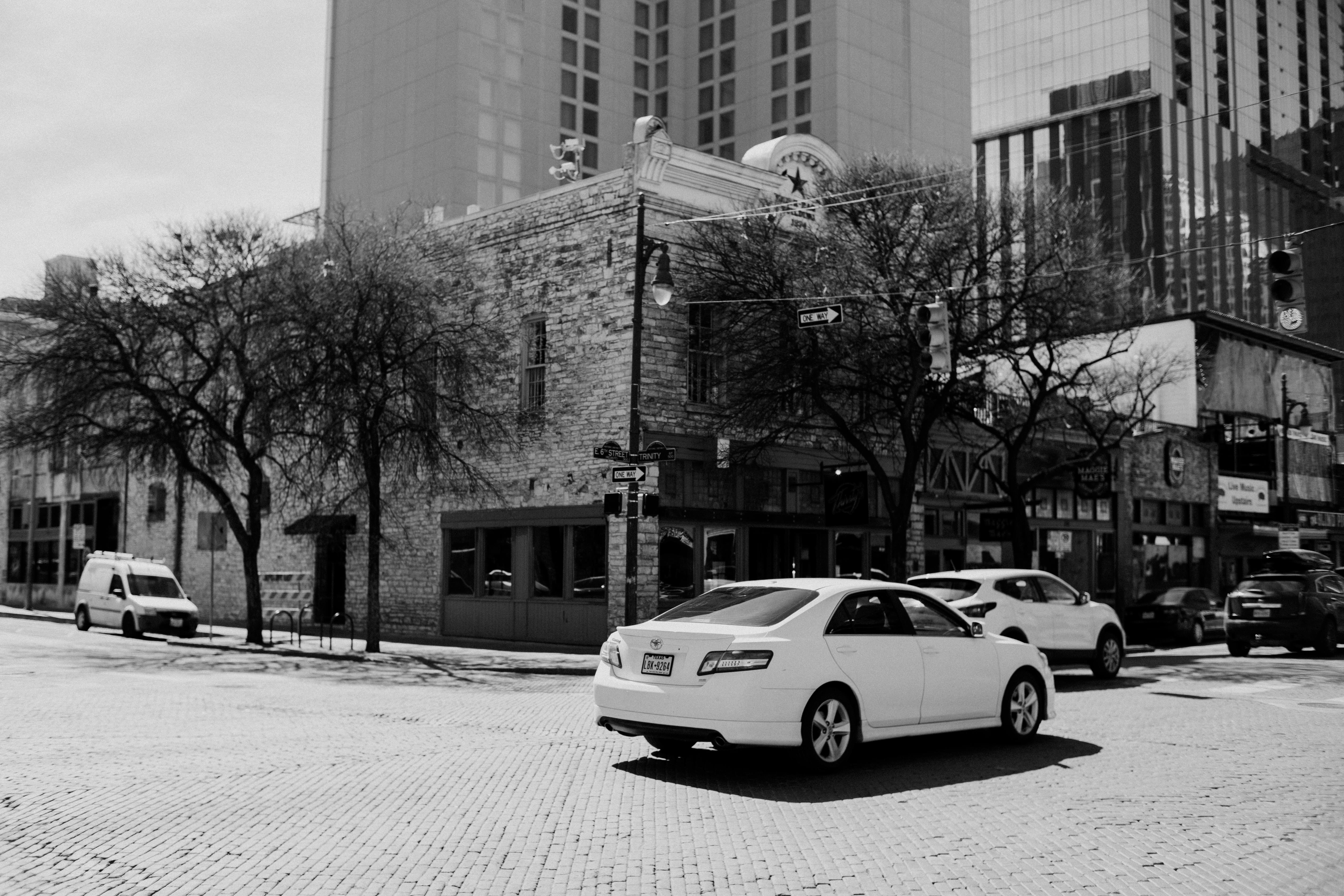 Cobblestone Crossroads: White Sedan Anchors a Quiet Monochrome City Scene