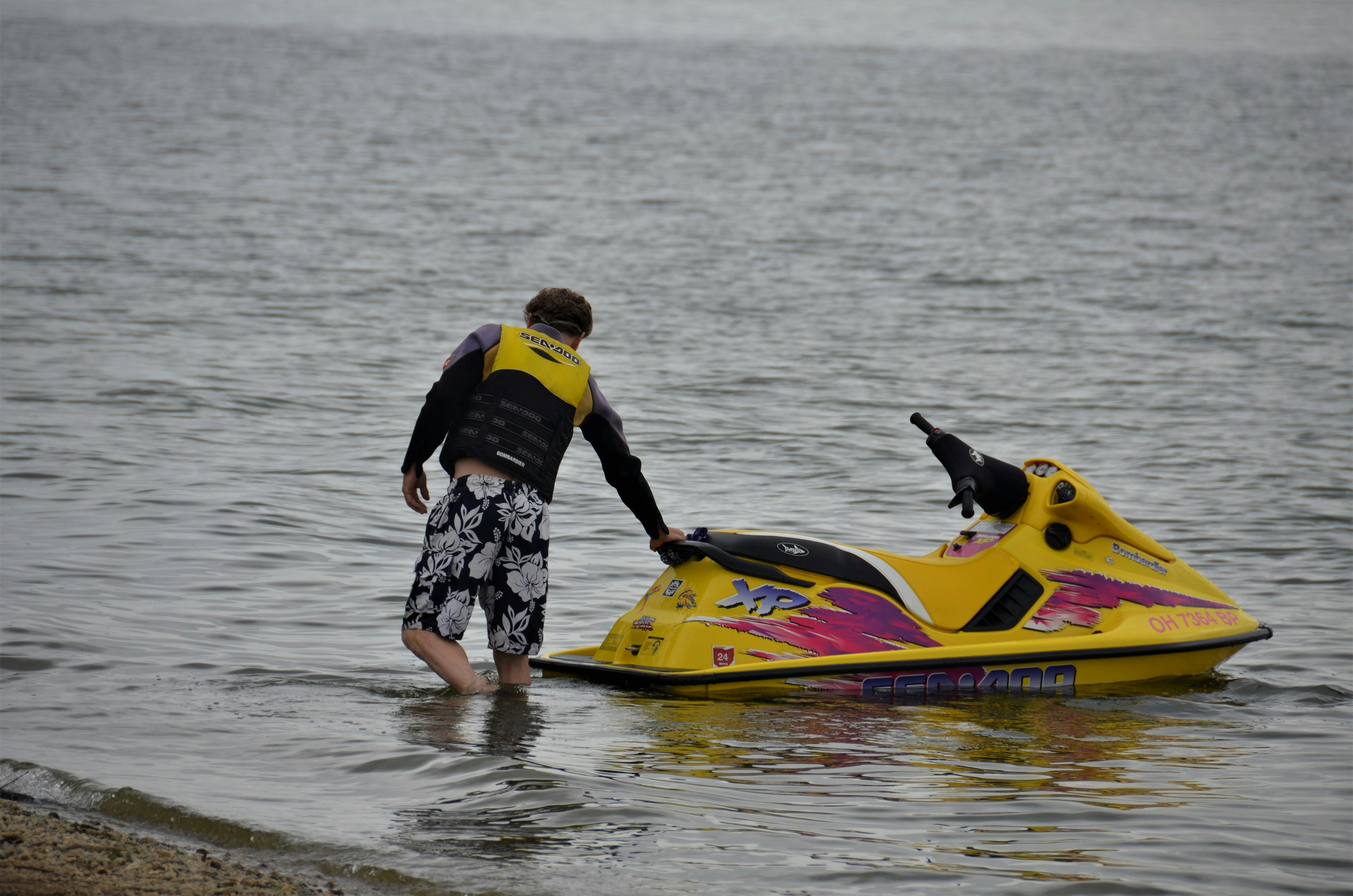 Person wading into shallow water beside a bright yellow jet ski, readying for a day of water sports.