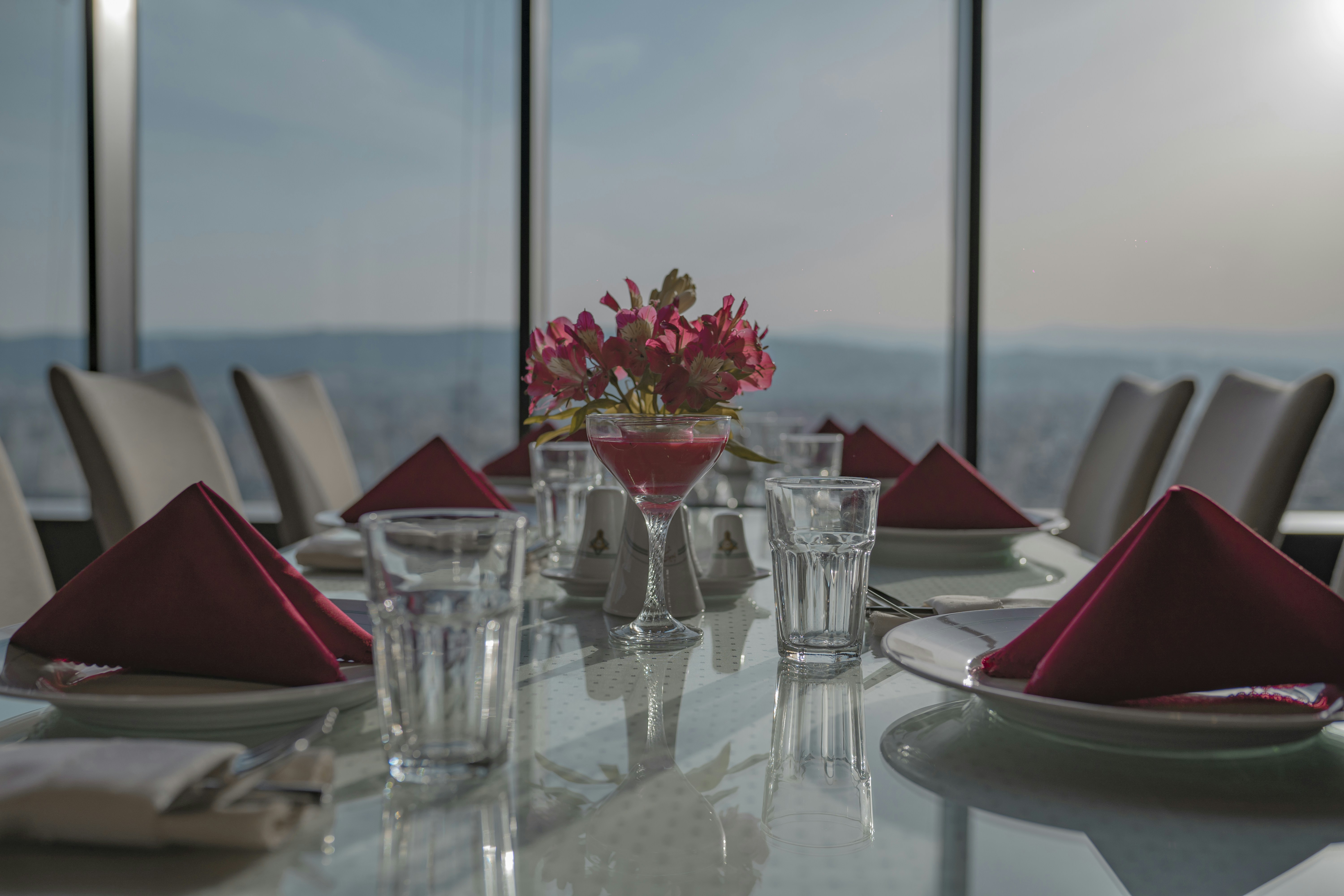 Elegant dining setup featuring a centerpiece of flowers and neatly arranged tableware with a panoramic view in the background.