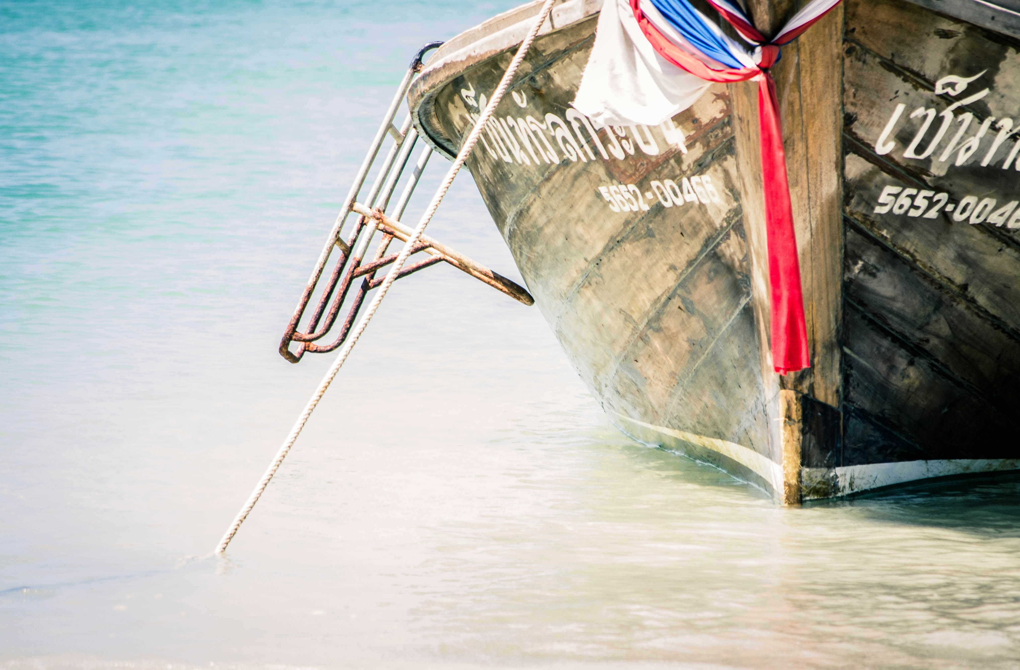 Traditional wooden boat anchored in shallow turquoise waters, adorned with colorful ribbons. The serene scene captures the essence of coastal tranquility.