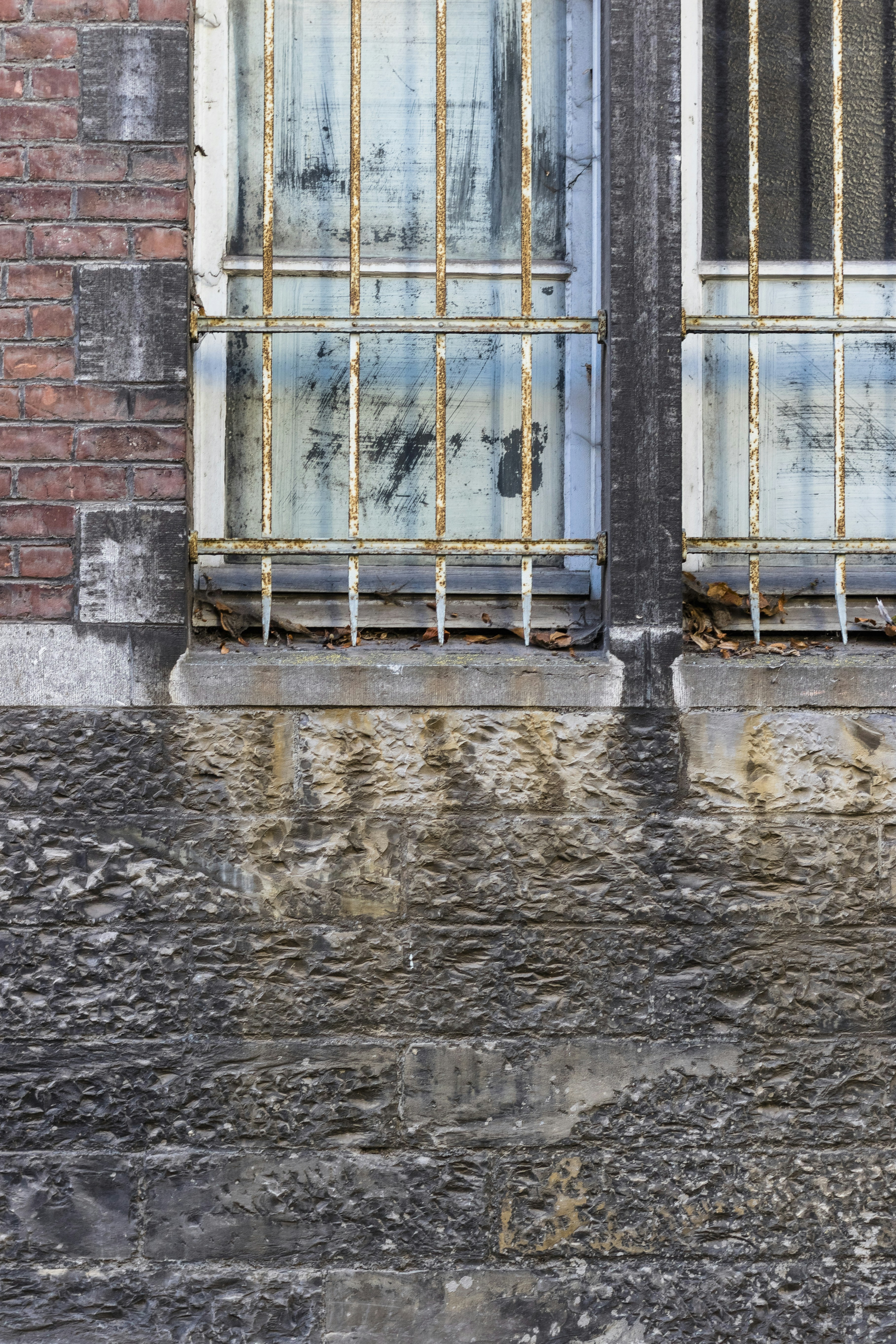 Weathered windows with rusty bars set against a textured wall, revealing the passage of time and neglect.