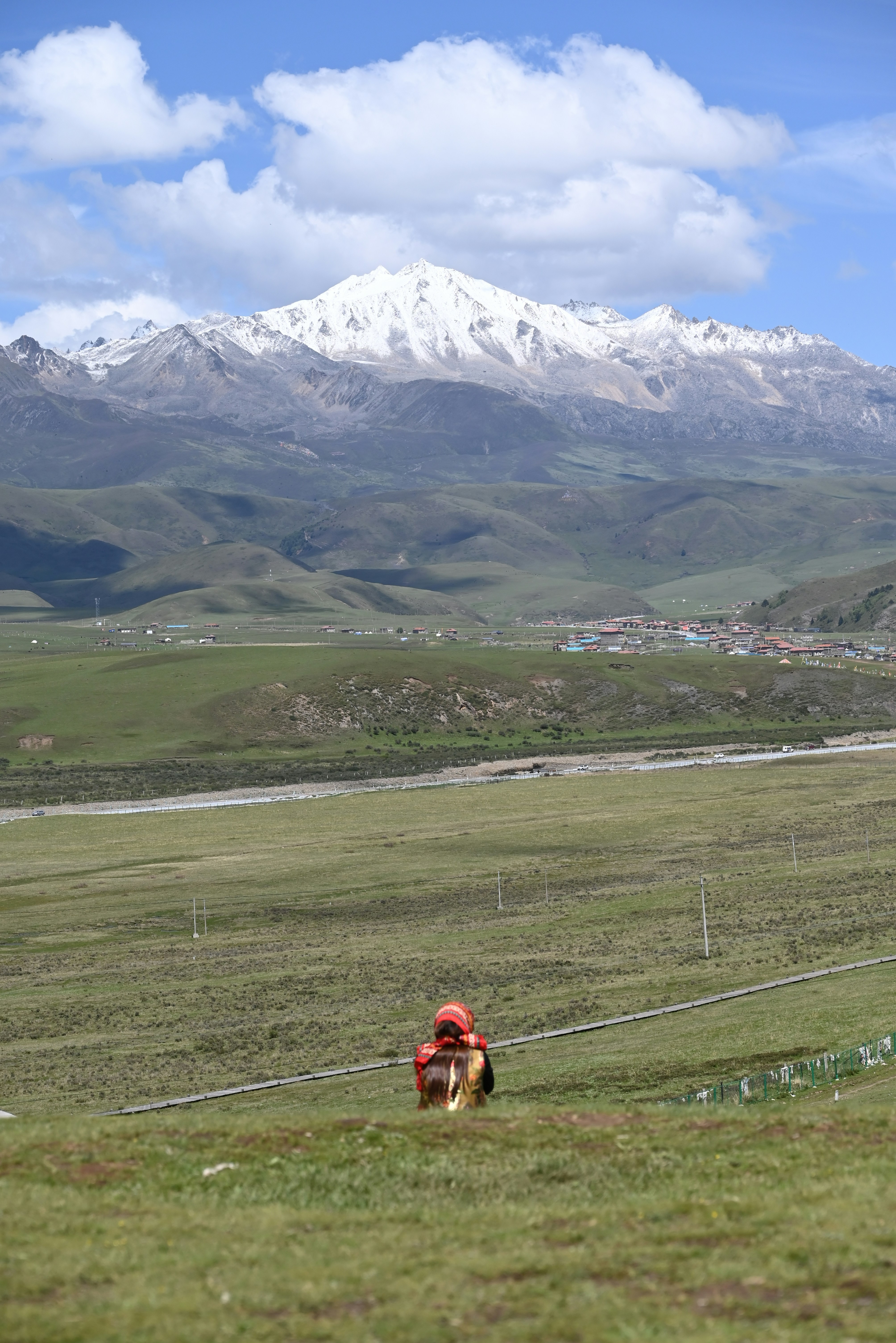 Red-helmeted rider traverses emerald valley toward snow-dusted peaks