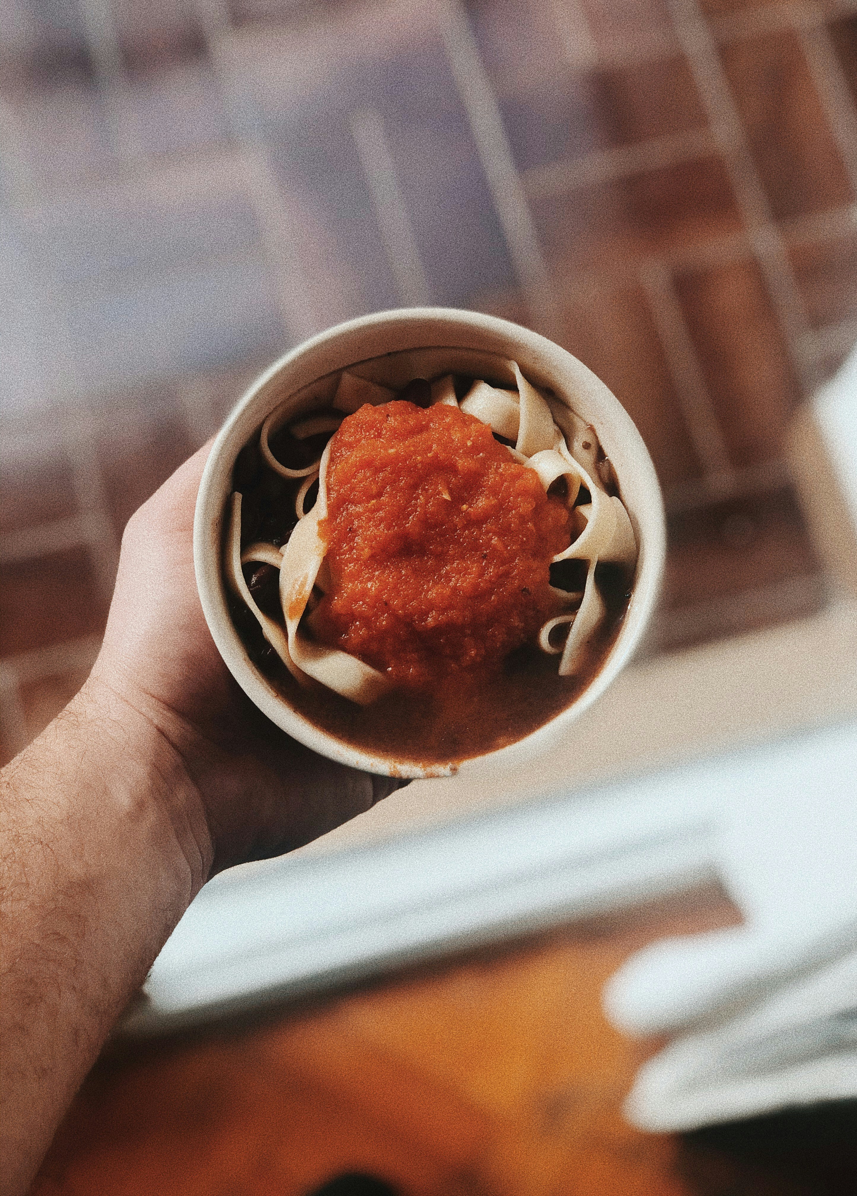 Handheld bowl of pappardelle topped with vibrant tomato sauce, set against a textured background.