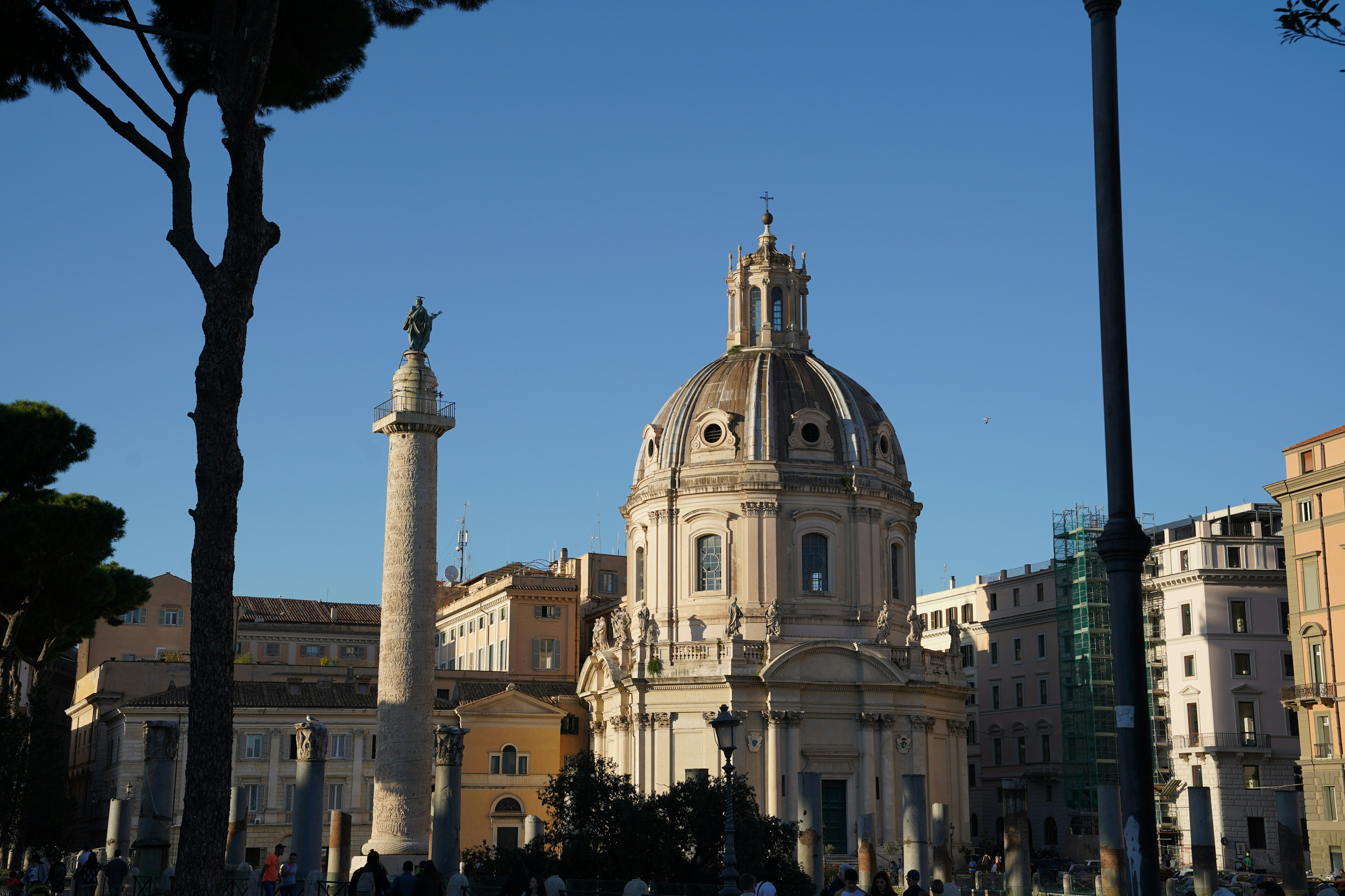 Baroque dome of the Church of Santa Maria di Loreto framed by historic columns and modern architecture under a clear blue sky.