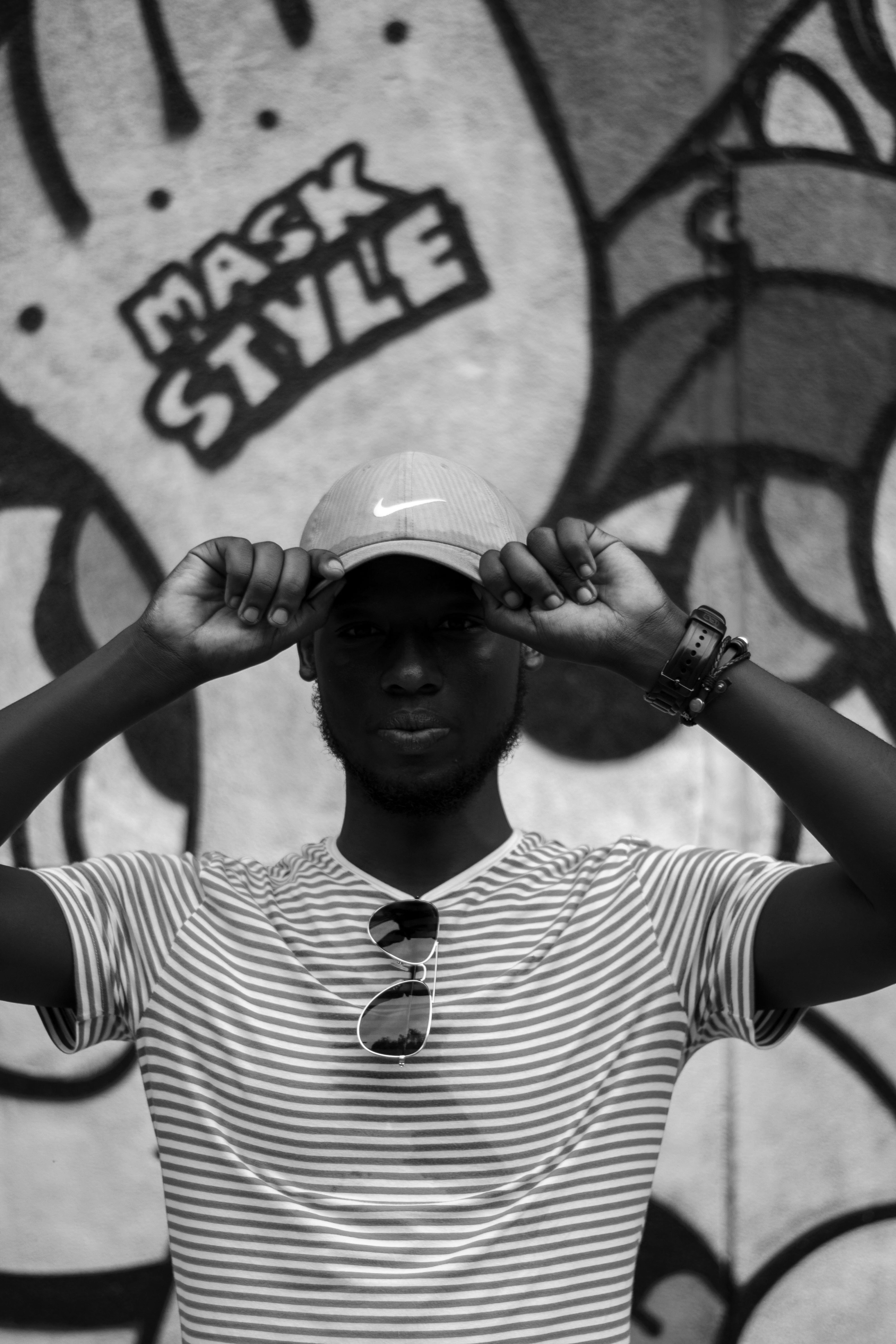 A young man wearing a striped shirt and cap poses confidently against a vibrant graffiti backdrop featuring the words 'MASK STYLE.'