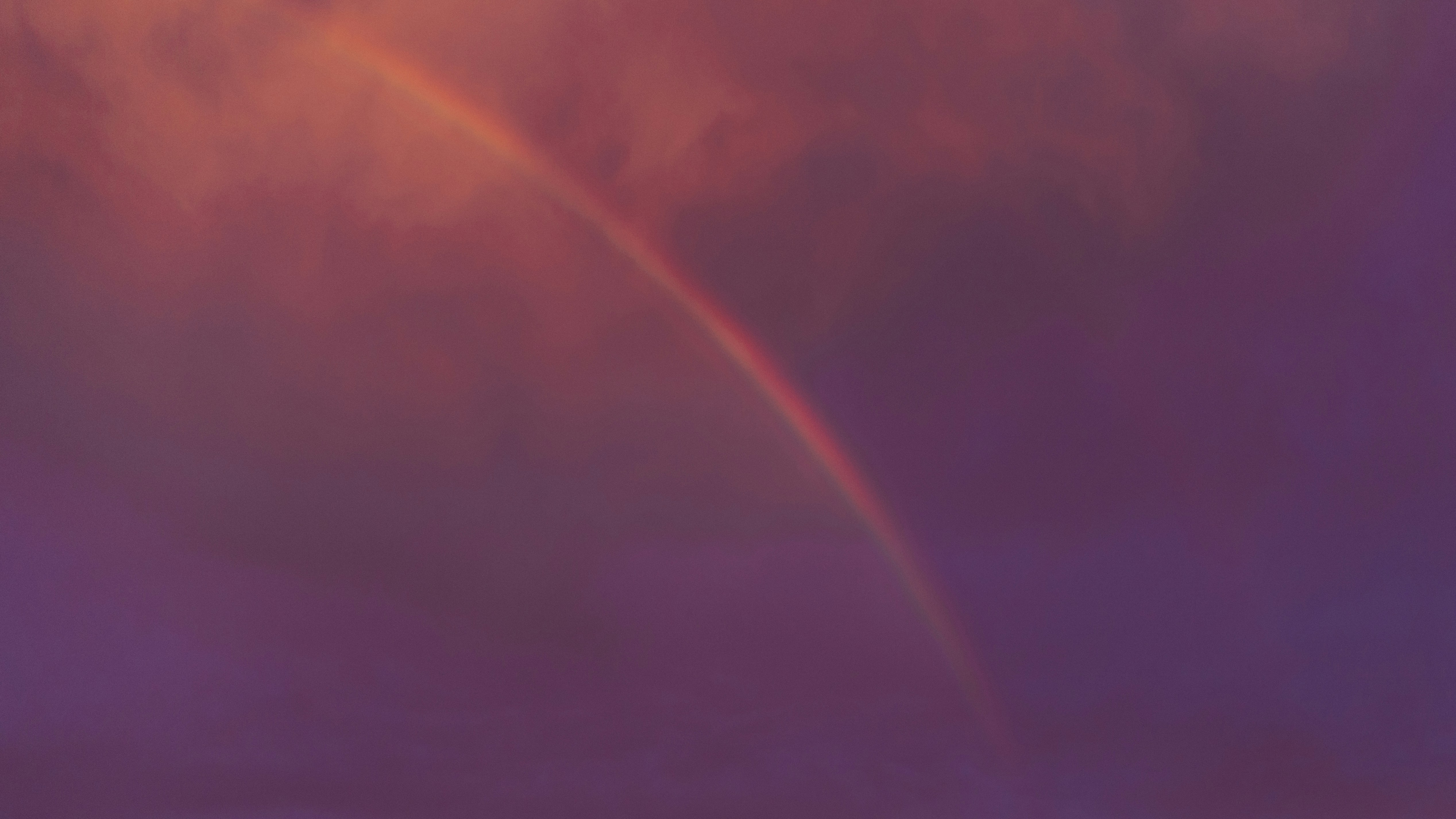 A vibrant rainbow arches gracefully through a dramatic sky filled with rich hues of purple and orange. 