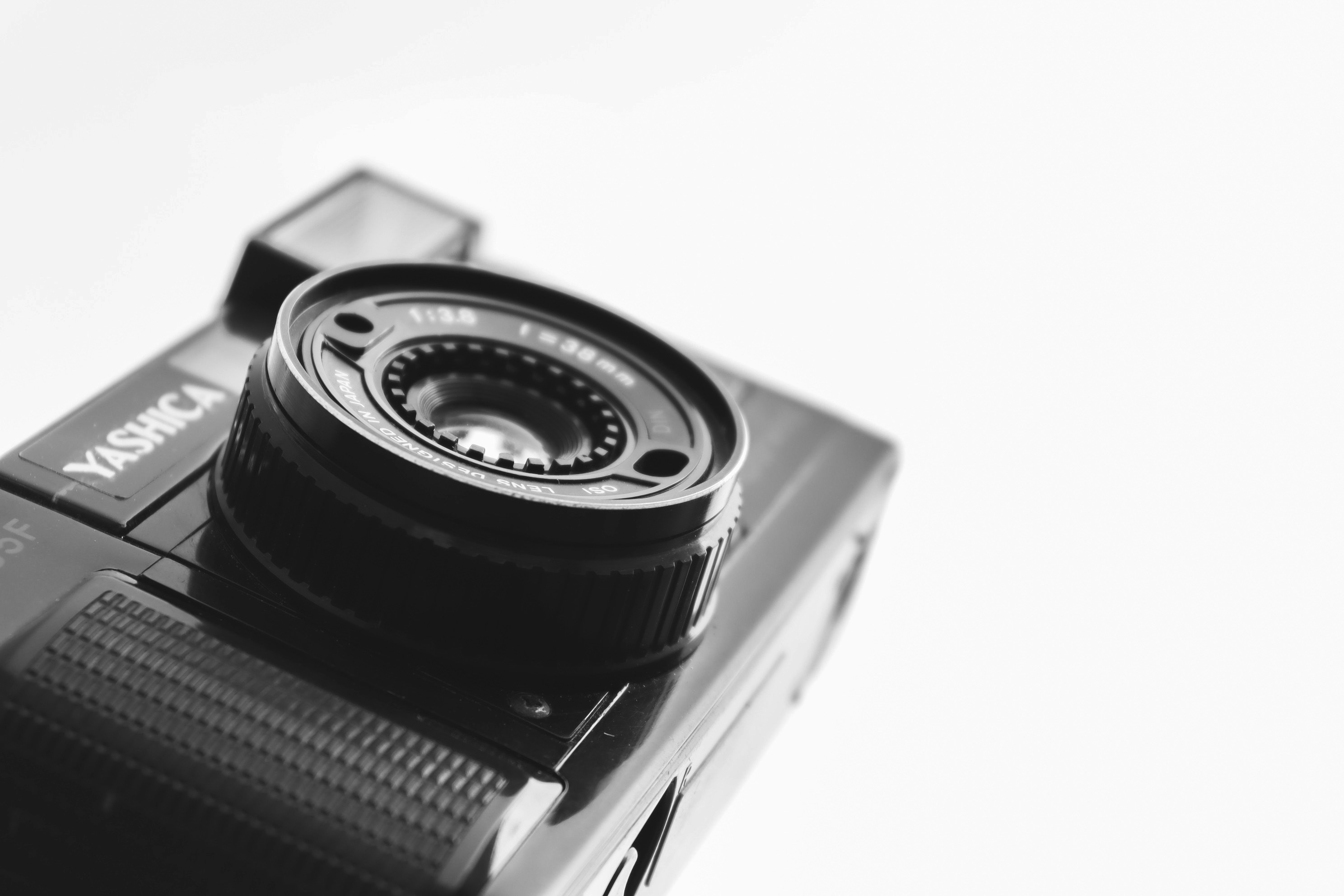 Black and silver Yashica analog film camera lens in sharp focus against a soft white background.