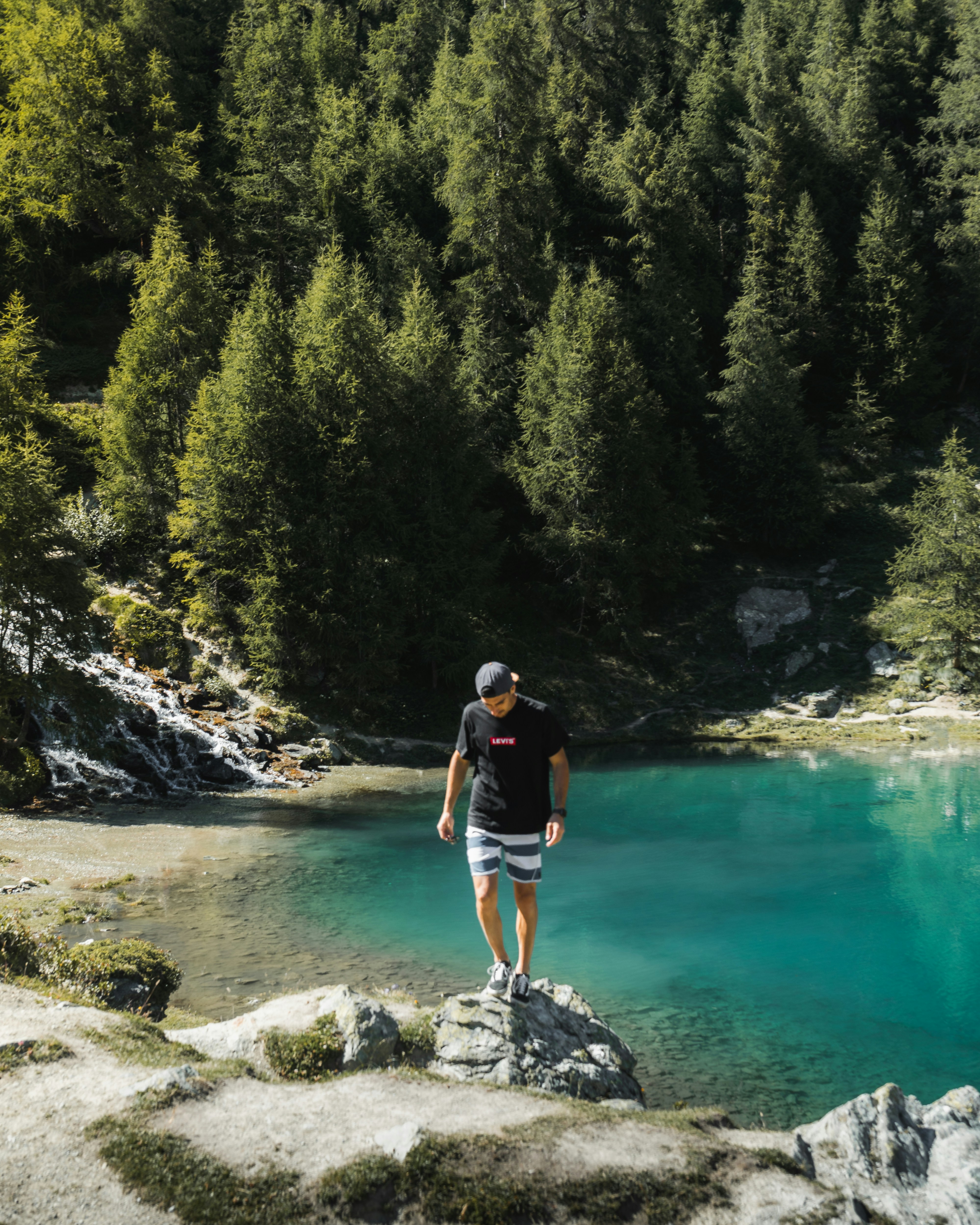 A lone explorer balances on a rocky ledge above a turquoise alpine lake