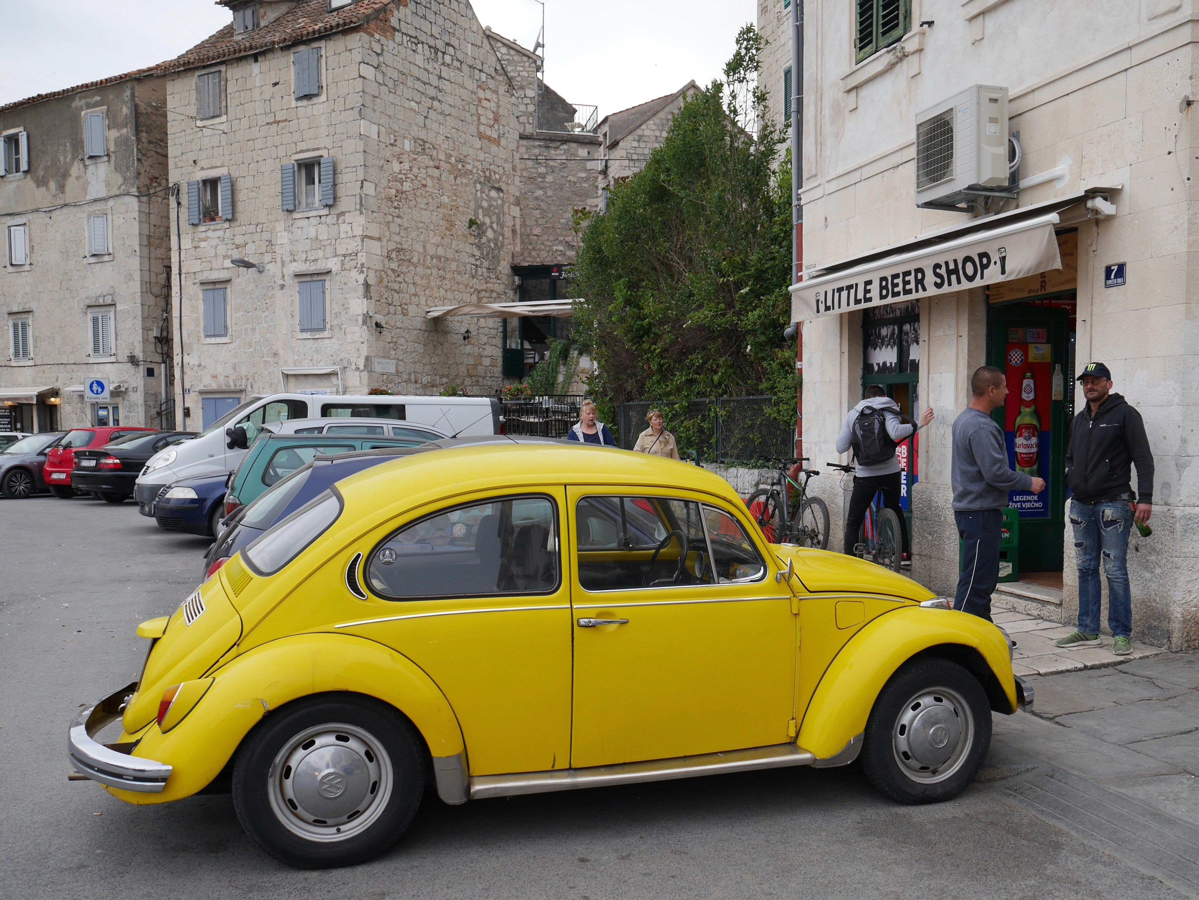 Yellow Velocità: A Classic Beetle Beside a Cobbled Town Shop