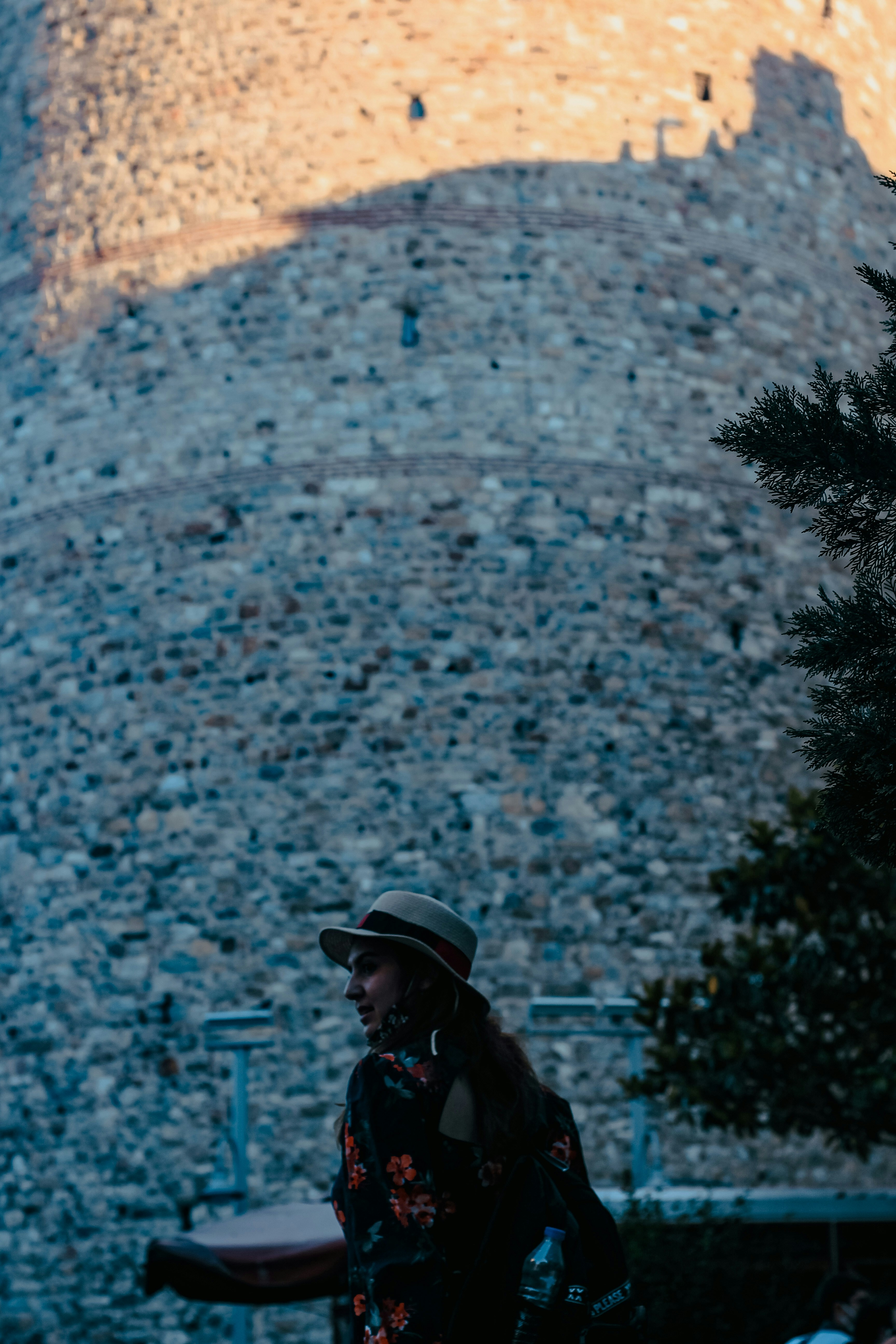Floral-clad traveler at the base of a sunlit fortress wall