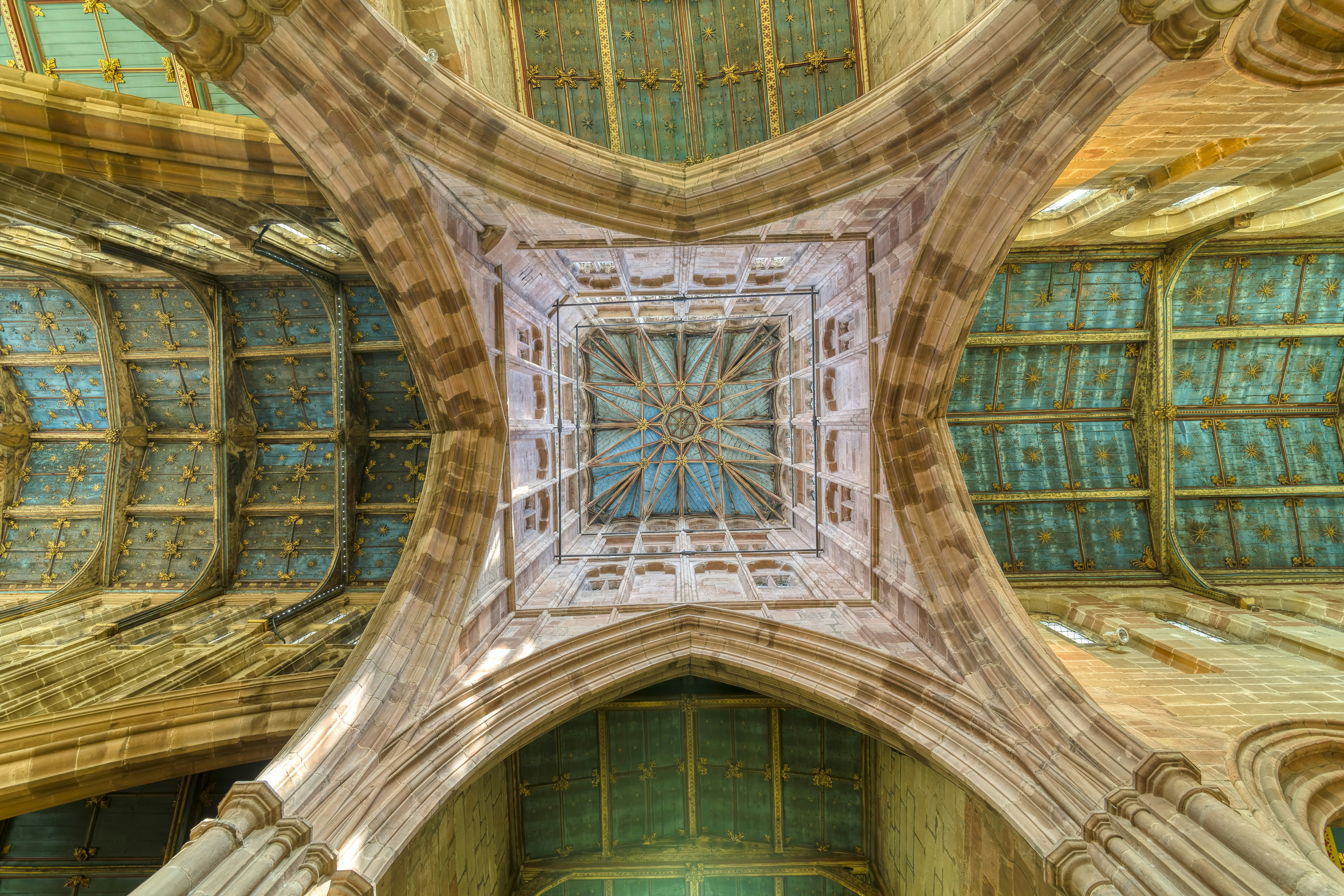 Intricate vaulted ceiling with ornate stone arches and teal panels, showcasing architectural symmetry.