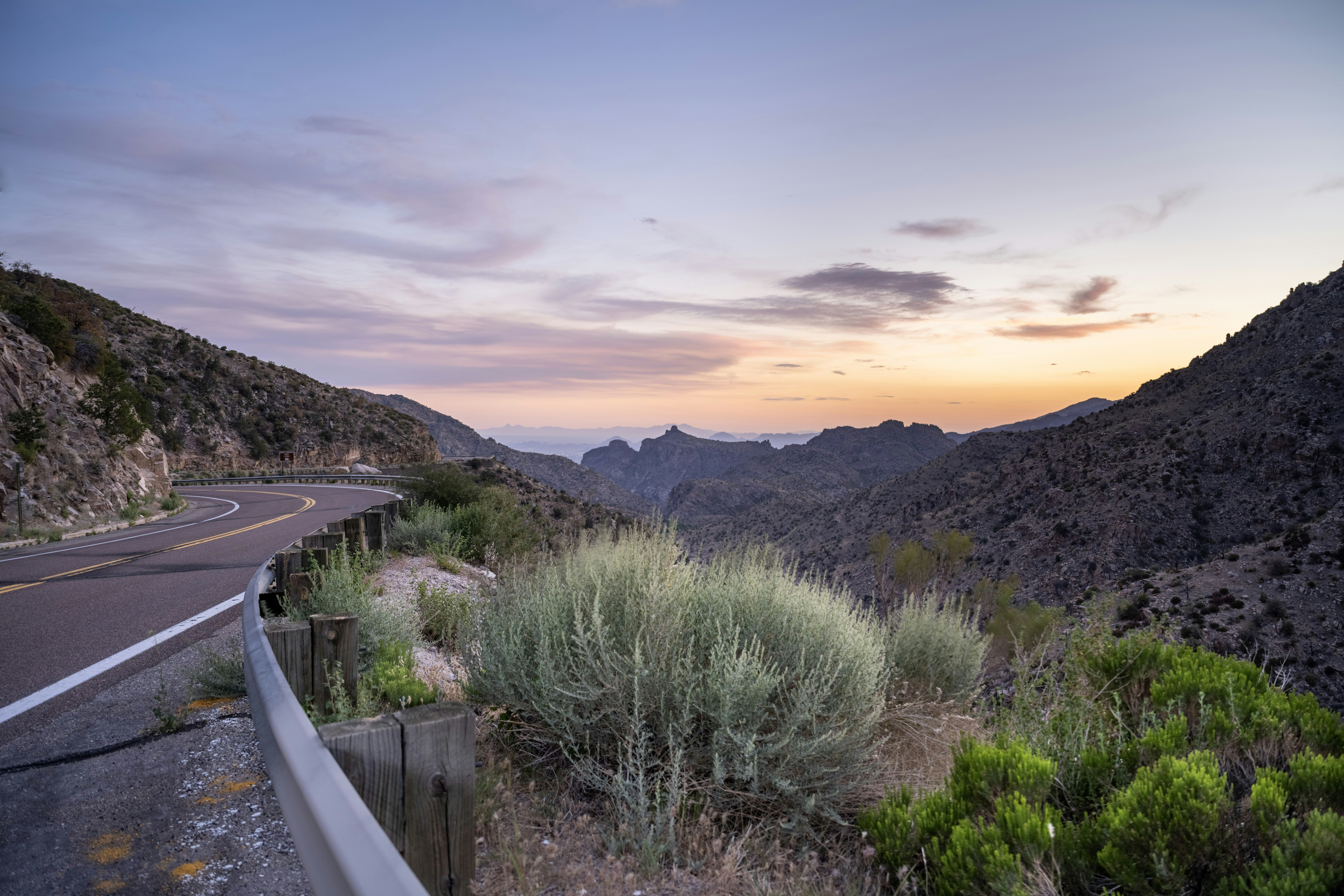 Winding road through rugged mountains with a vibrant sunset sky.