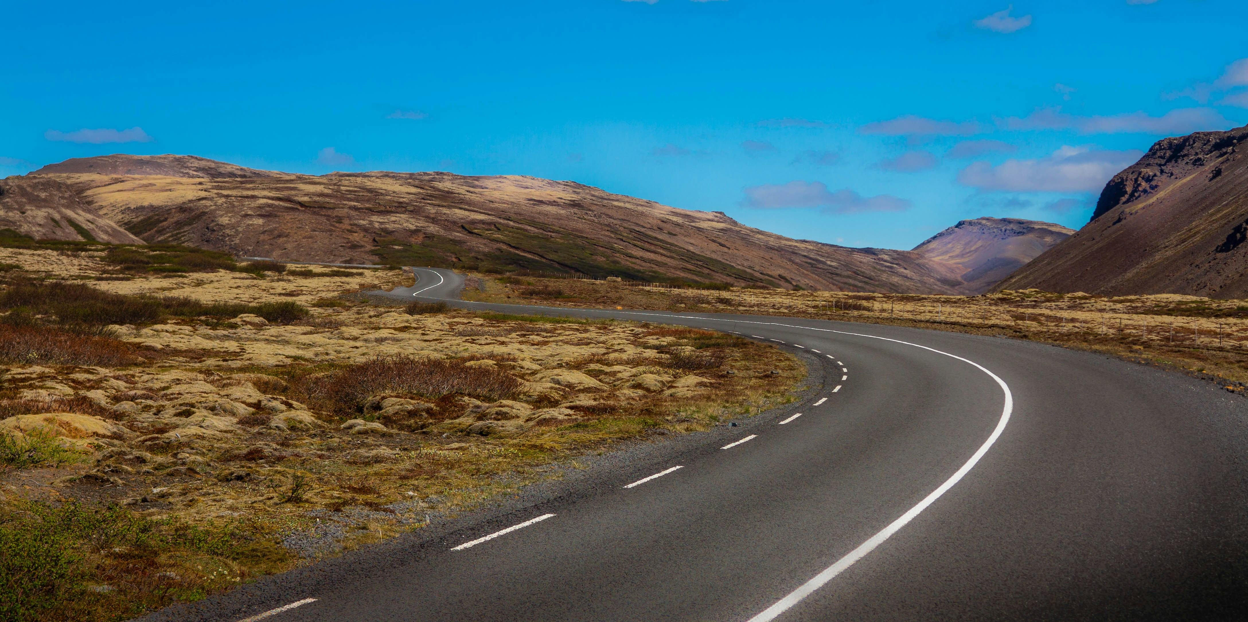 Curving road traversing a barren, golden-hued terrain under a clear blue sky.