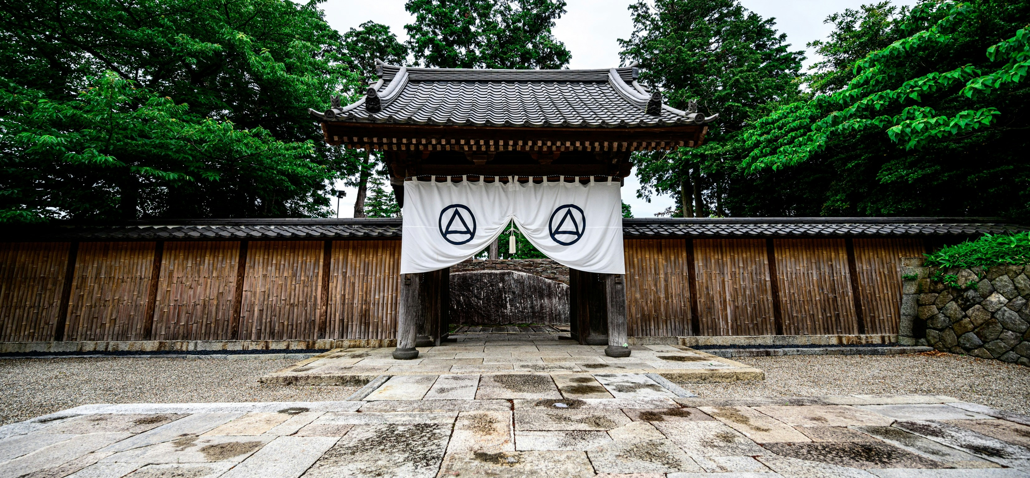 Quiet Portal at the Cedar Wall: White Bannered Gate Framed by Timber and Stone