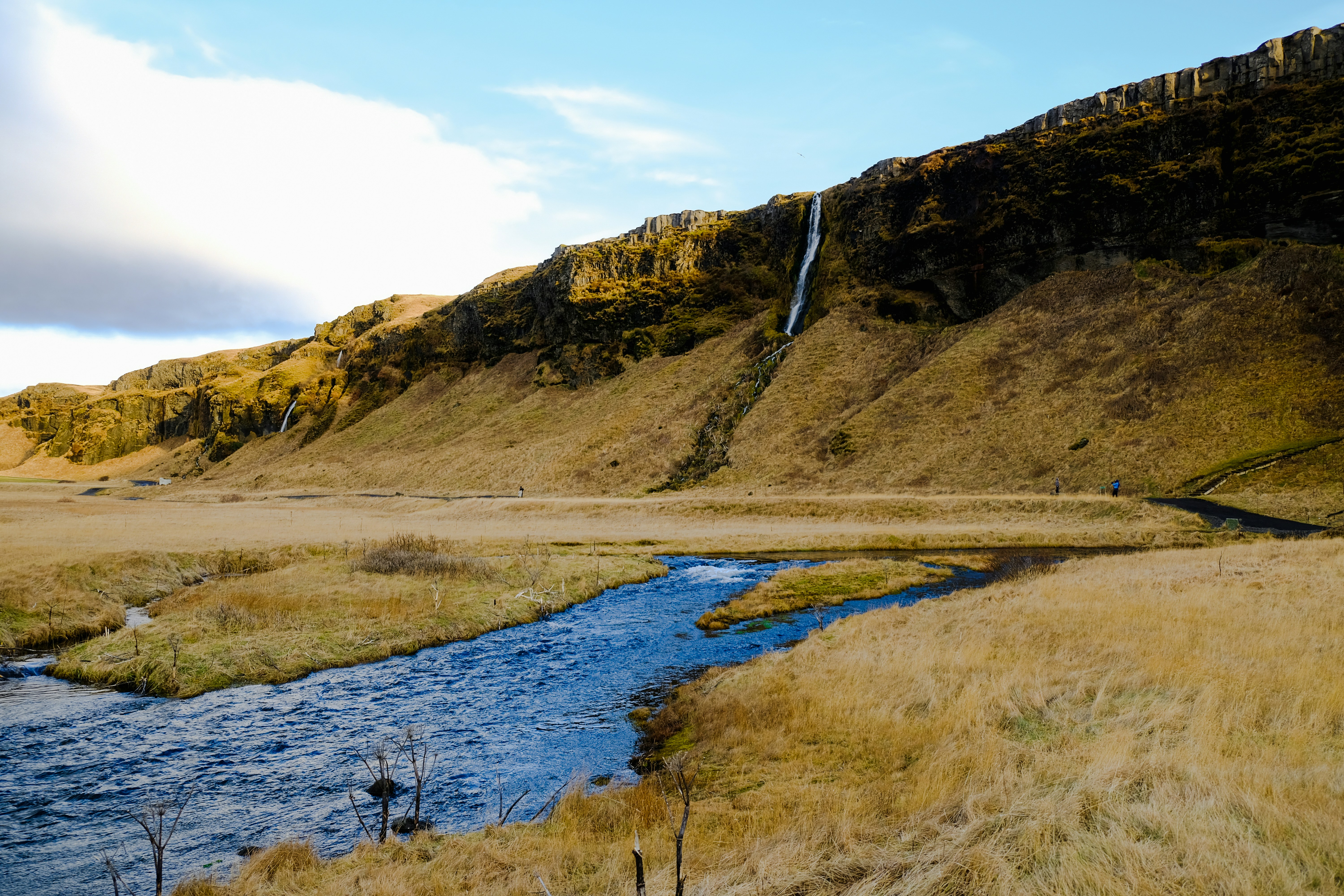 Edge of Light: A Narrow River Winding Under a Cliffside Waterfall
