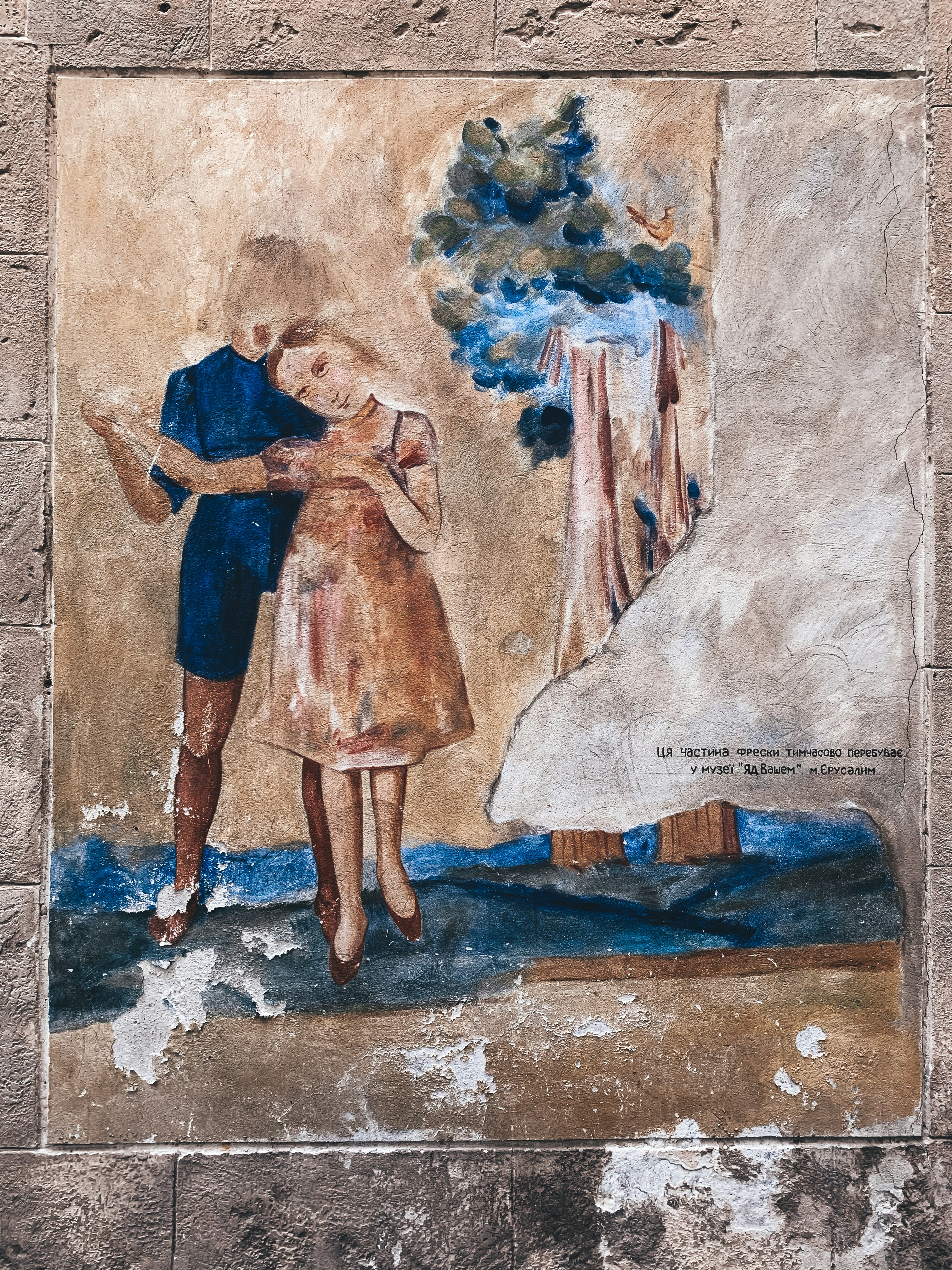 A mural depicting two children in a tender moment, surrounded by a lush tree and draped fabric. The artwork captures a nostalgic essence.