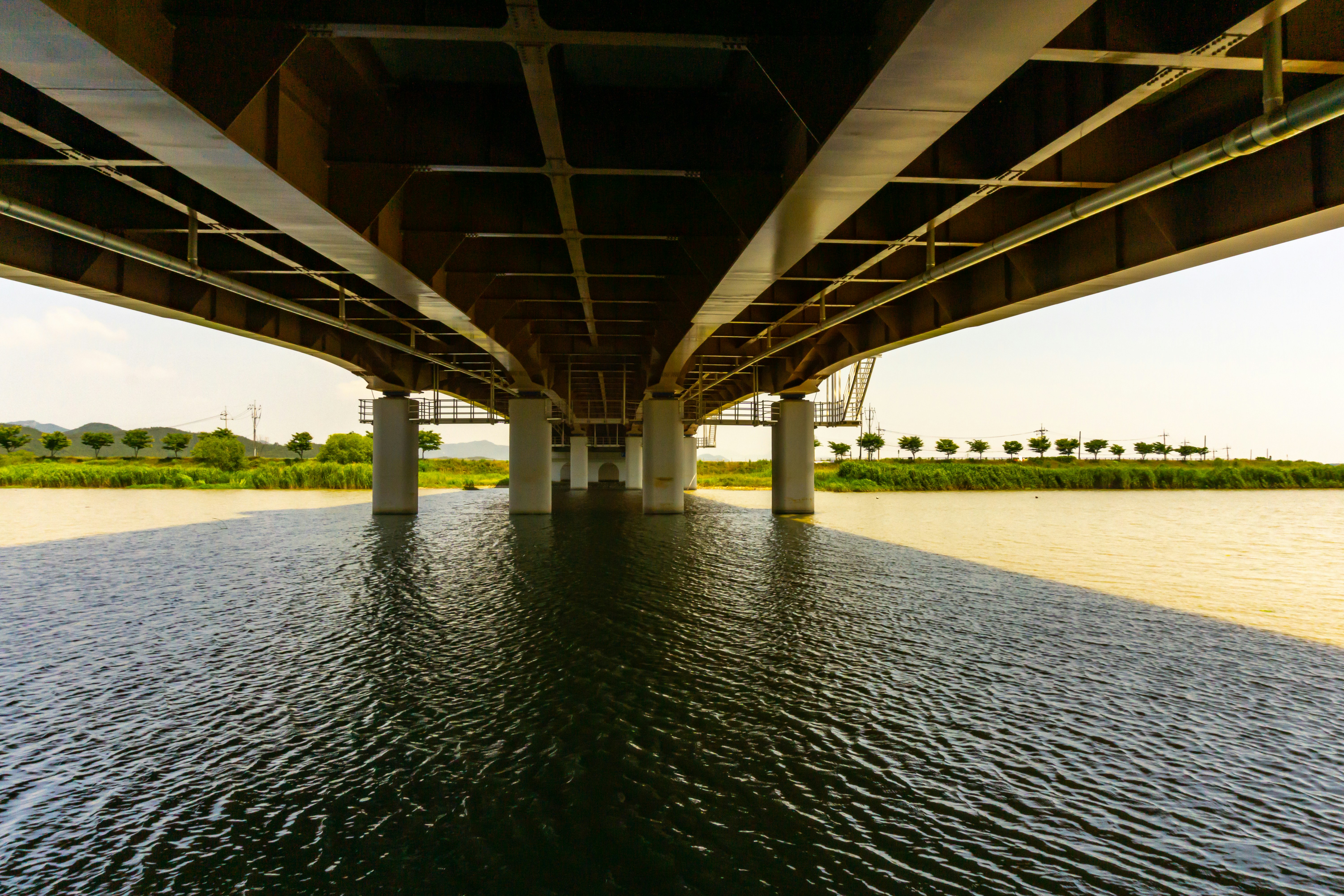 View from beneath a bridge, showcasing the intricate support structure and reflections in the water below.