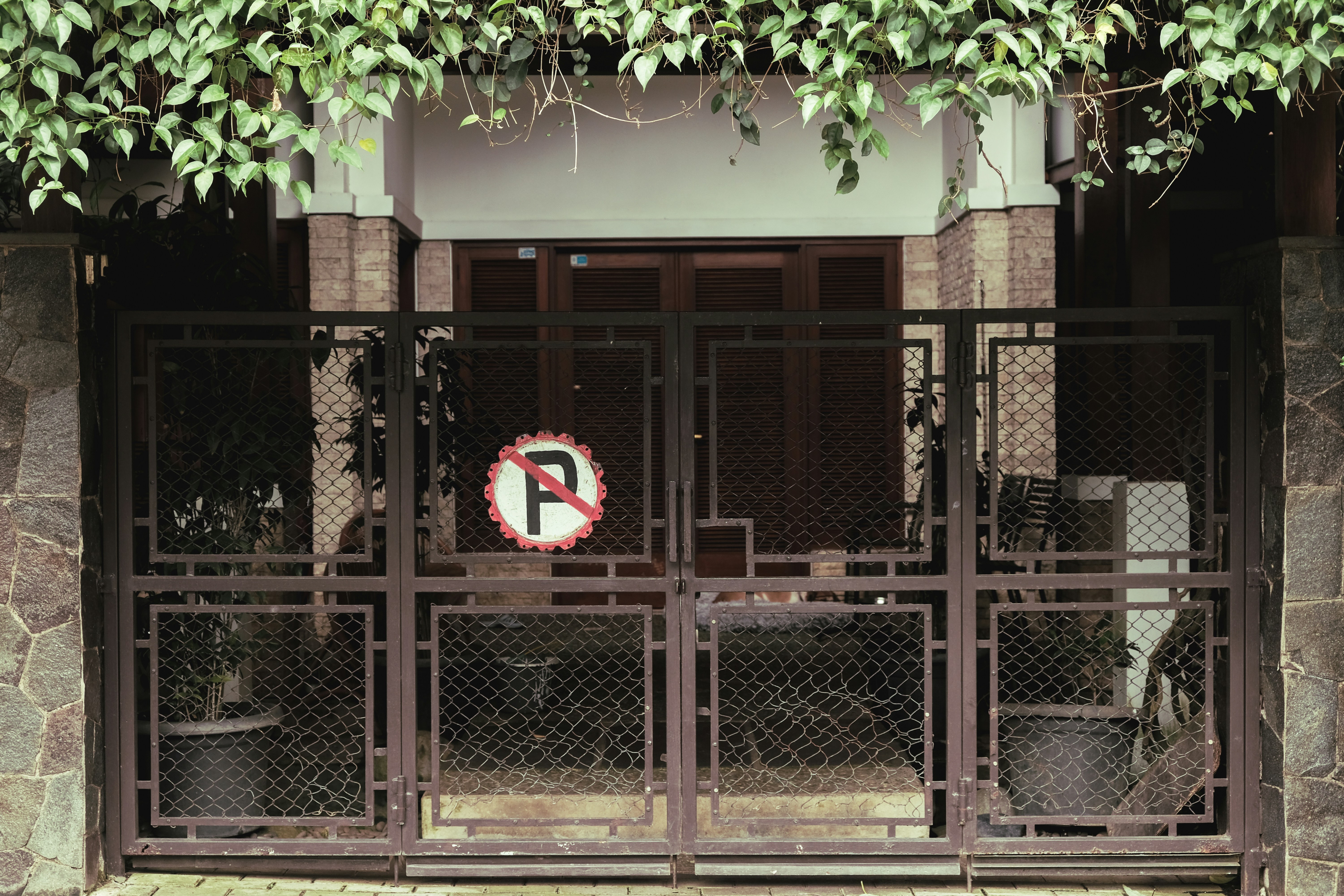 Intricate metal gate adorned with a no parking sign, framed by lush greenery above.