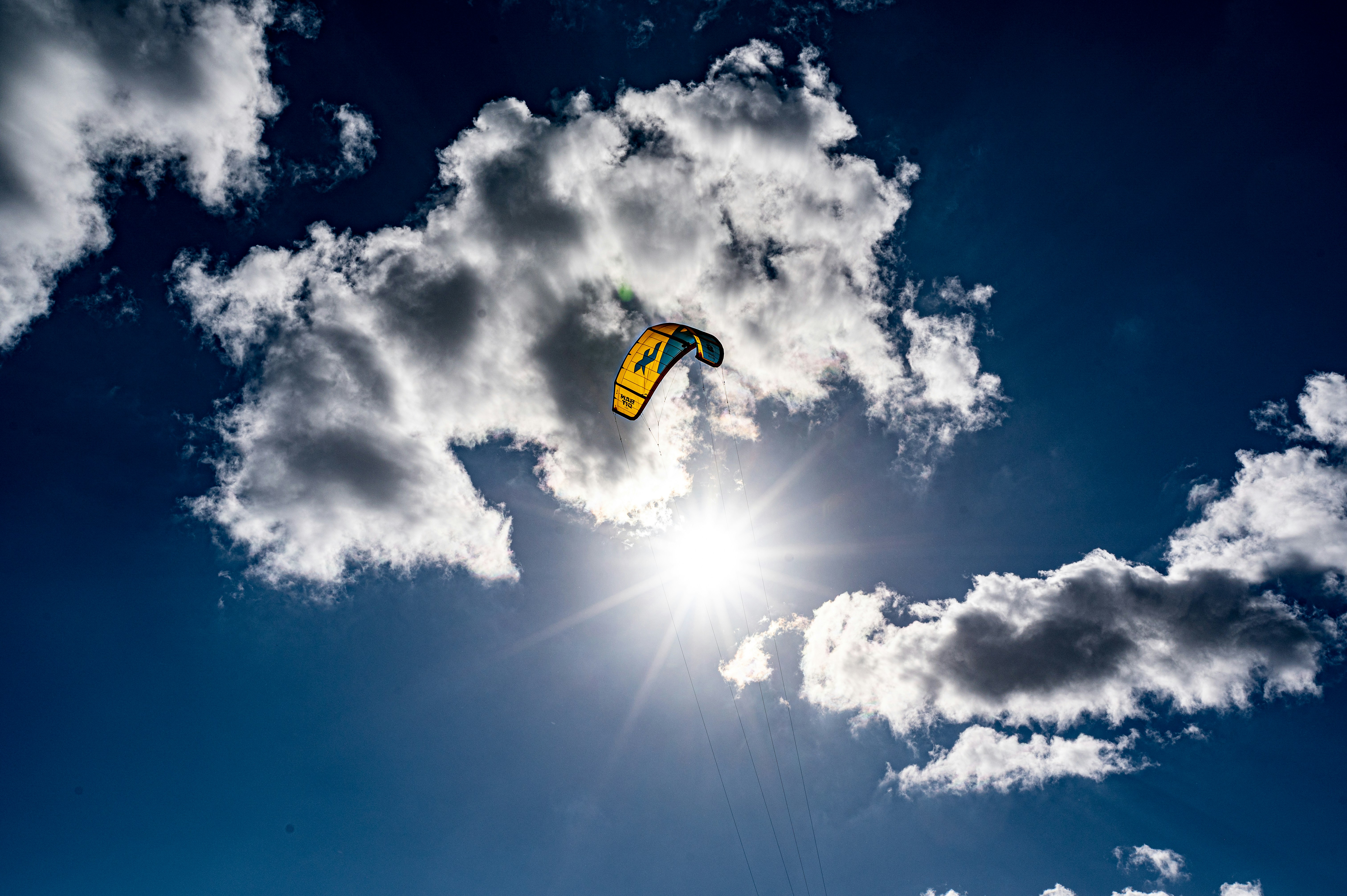 Sunlit Arc: A Yellow Paraglider Cuts Through Cloudbreak