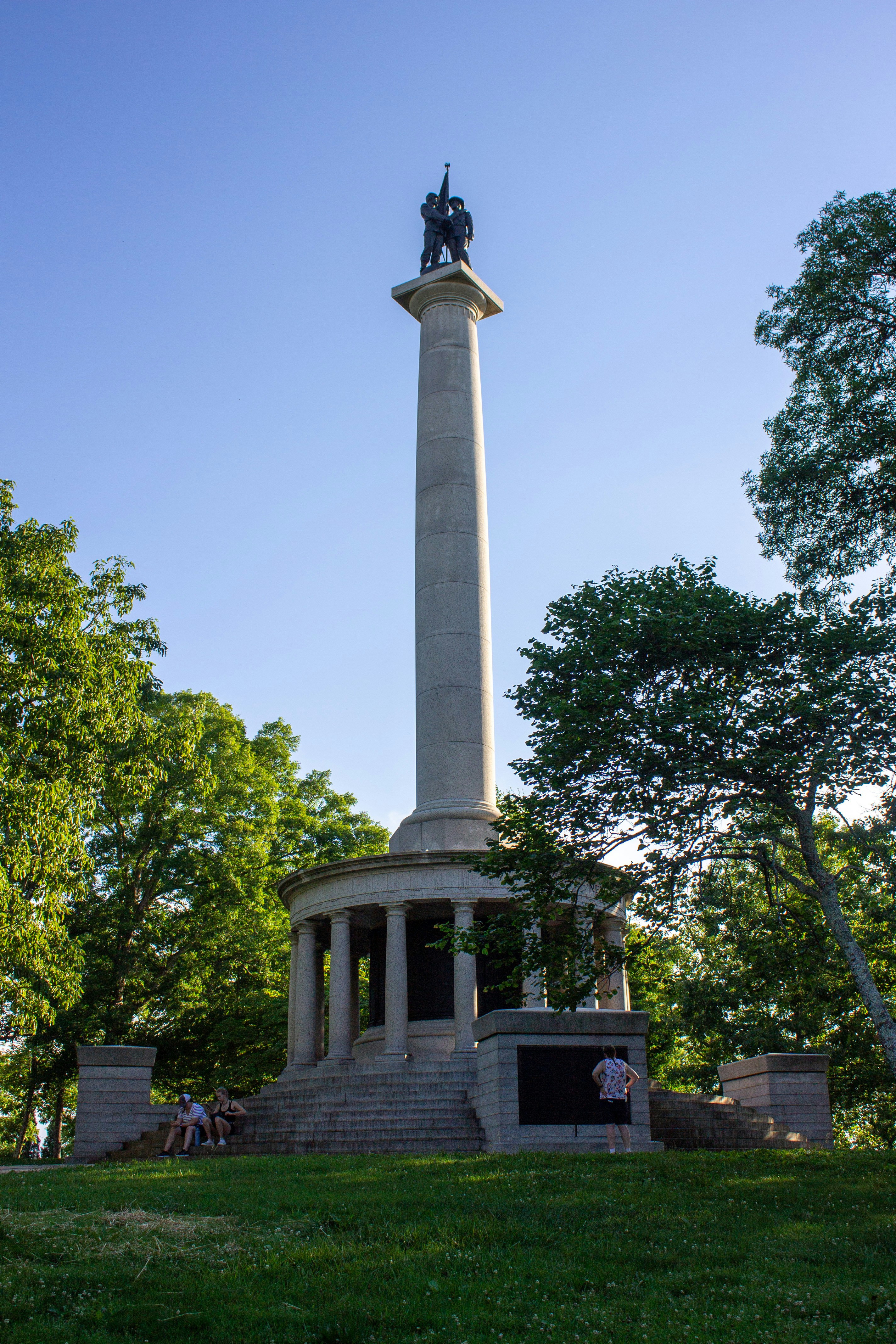 Tall memorial column crowned with a statue rises above a tree-lined park