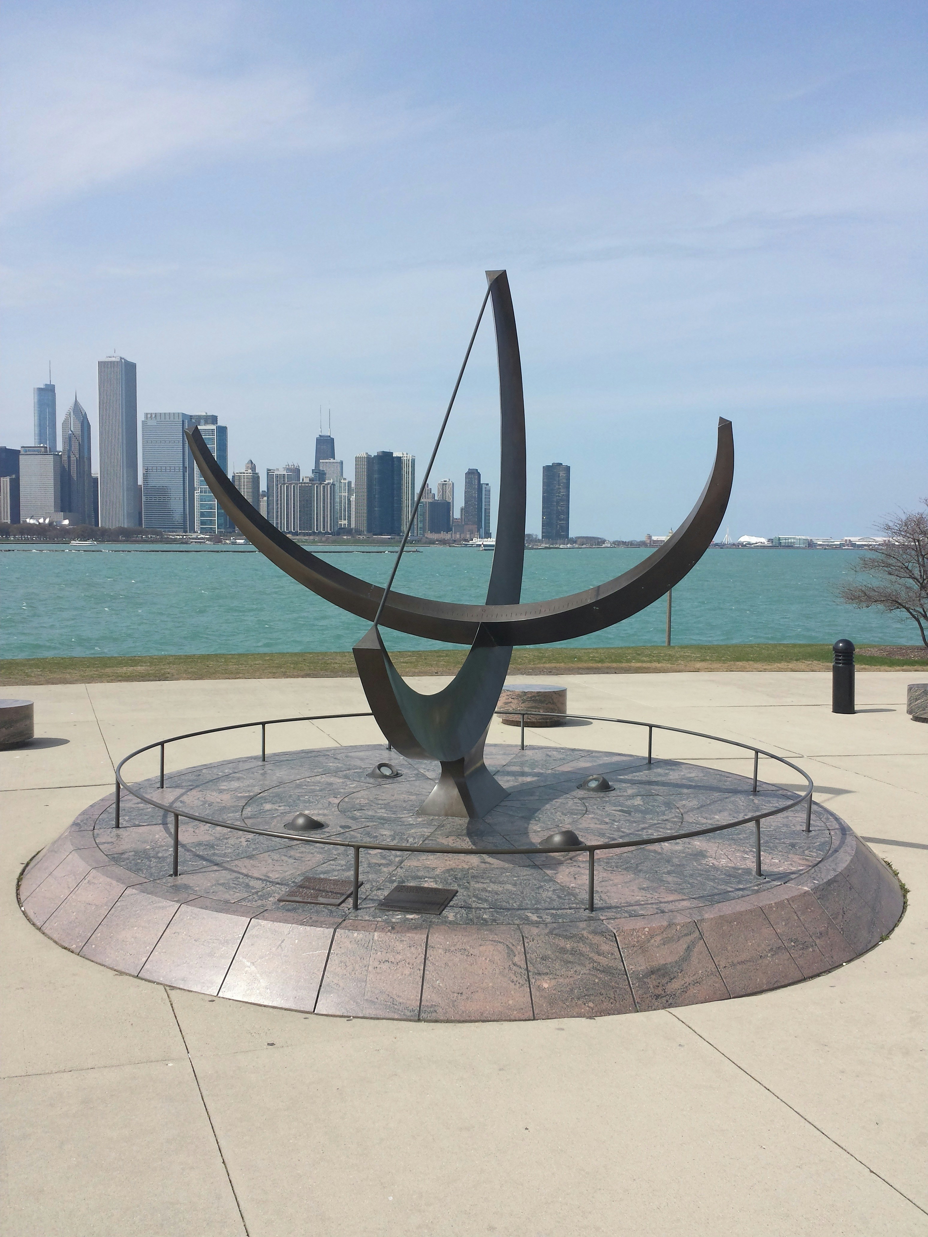 Sculptural sundial set against the Chicago skyline and Lake Michigan. The artwork blends nature and urban architecture seamlessly.