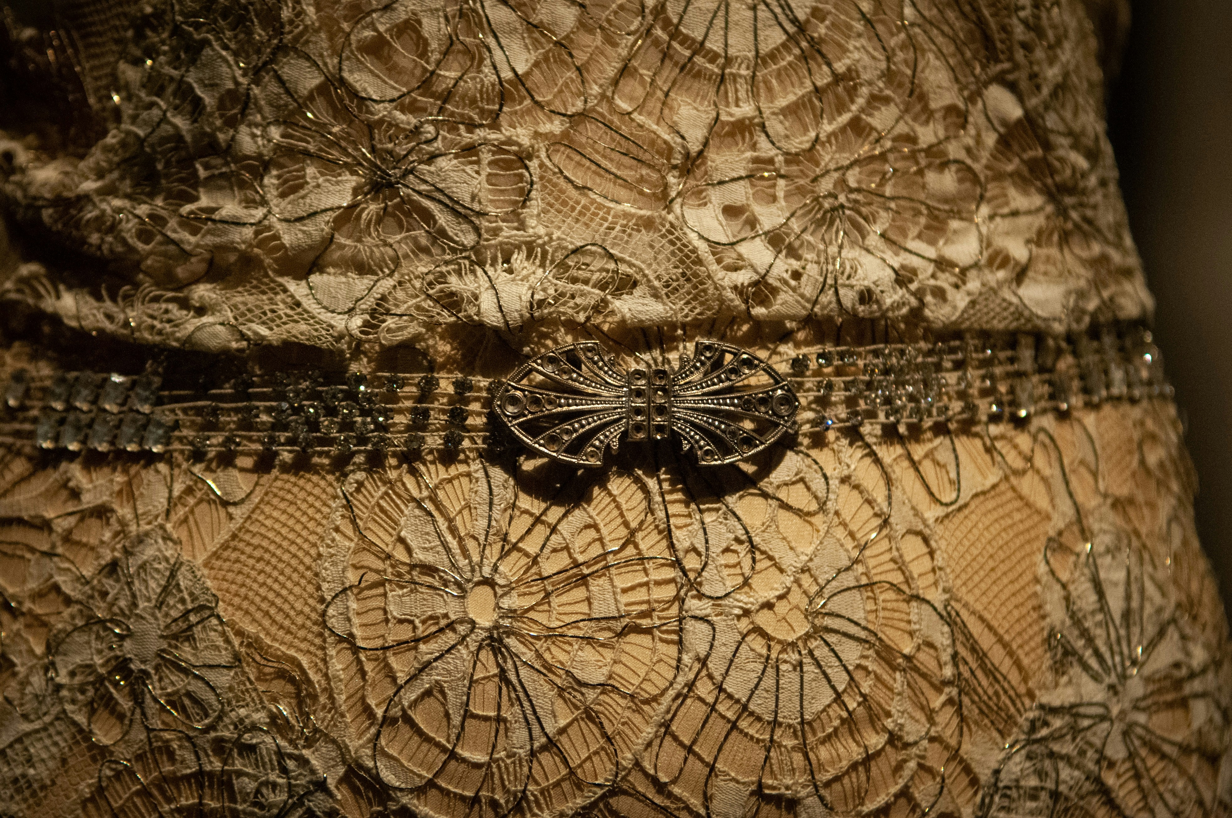 Close-up of a vintage belt featuring a decorative buckle, set against a backdrop of delicate lace fabric. The intricate design highlights the craftsmanship of the piece.