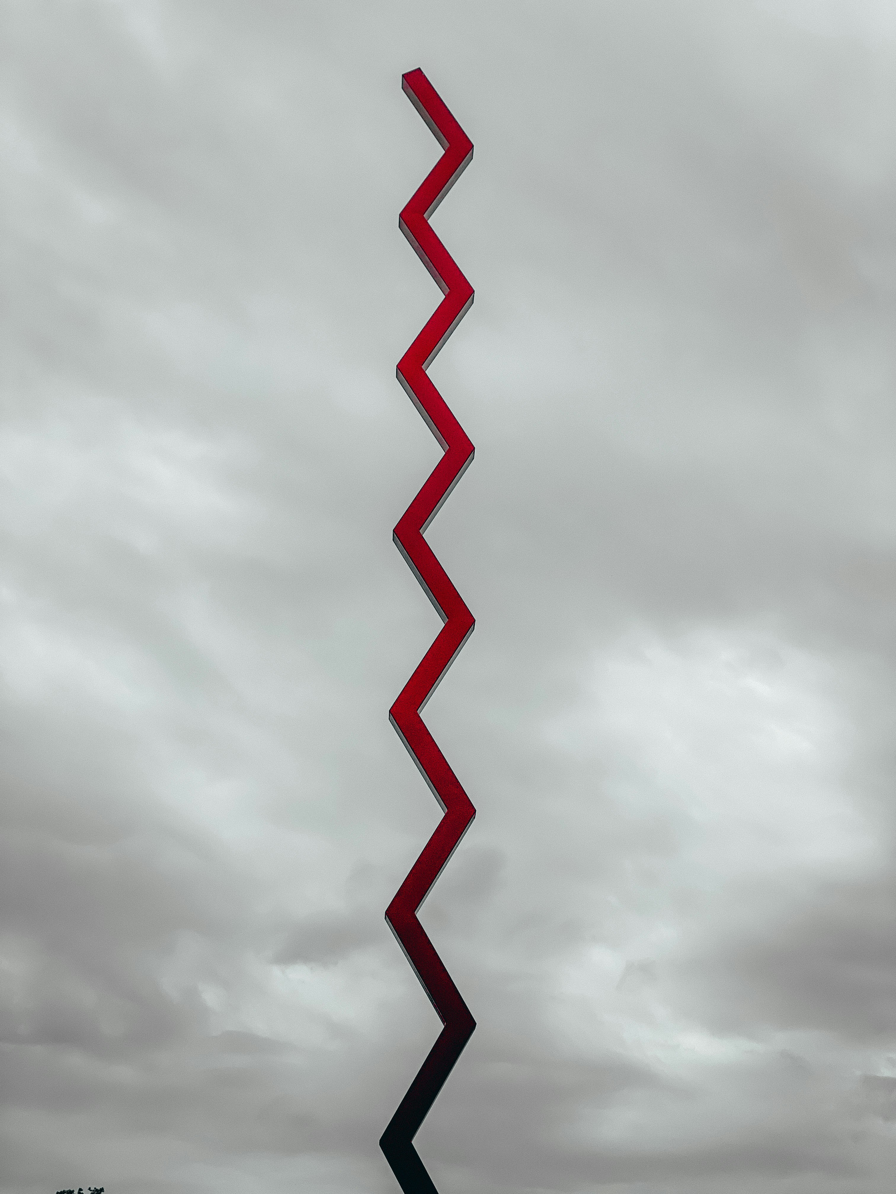 Bold red zigzag sculpture rises dramatically against a cloudy backdrop, emphasizing modern artistic expression.