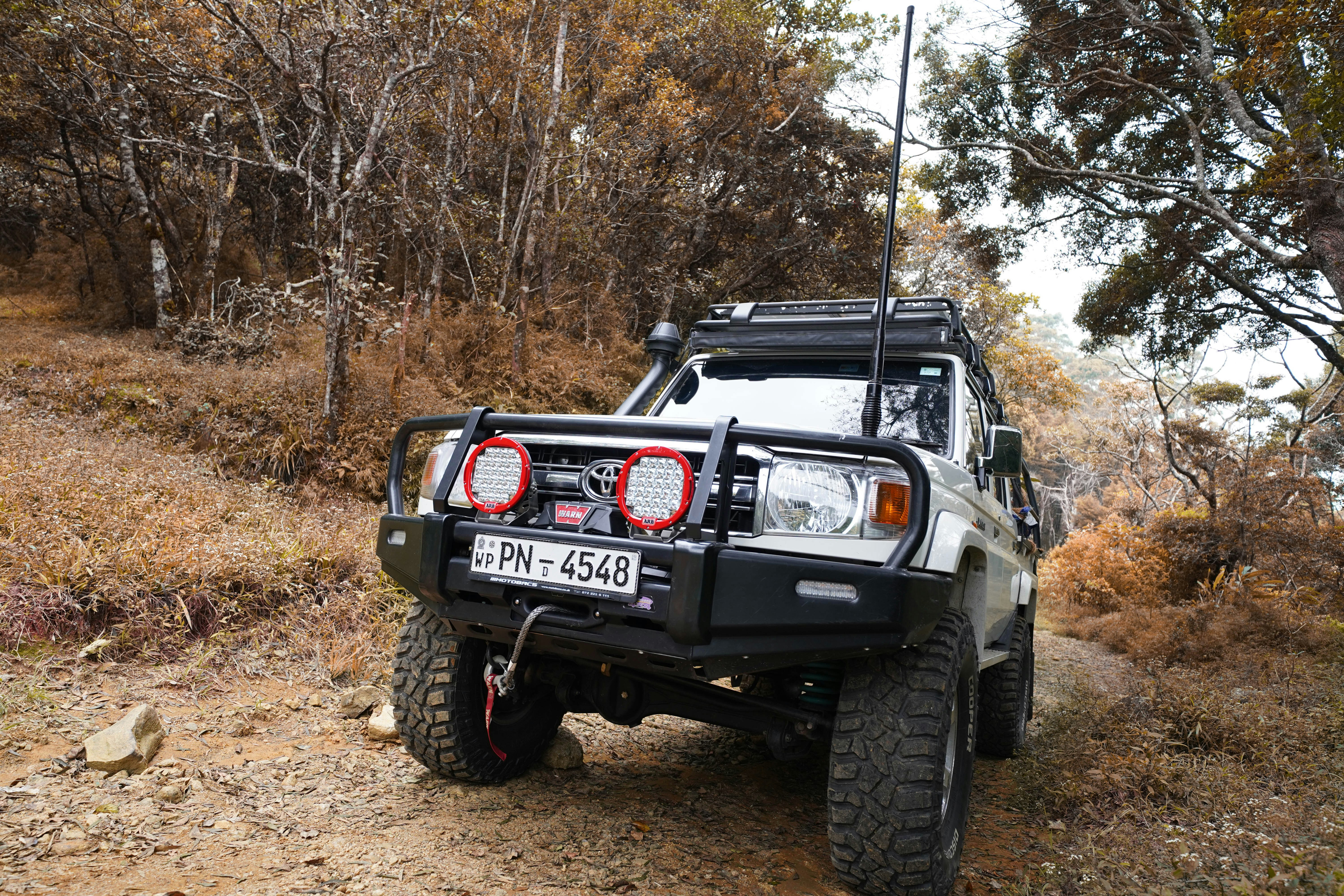 Off-road vehicle parked on a rugged trail surrounded by autumn foliage. The powerful design and accessories highlight its readiness for adventure.