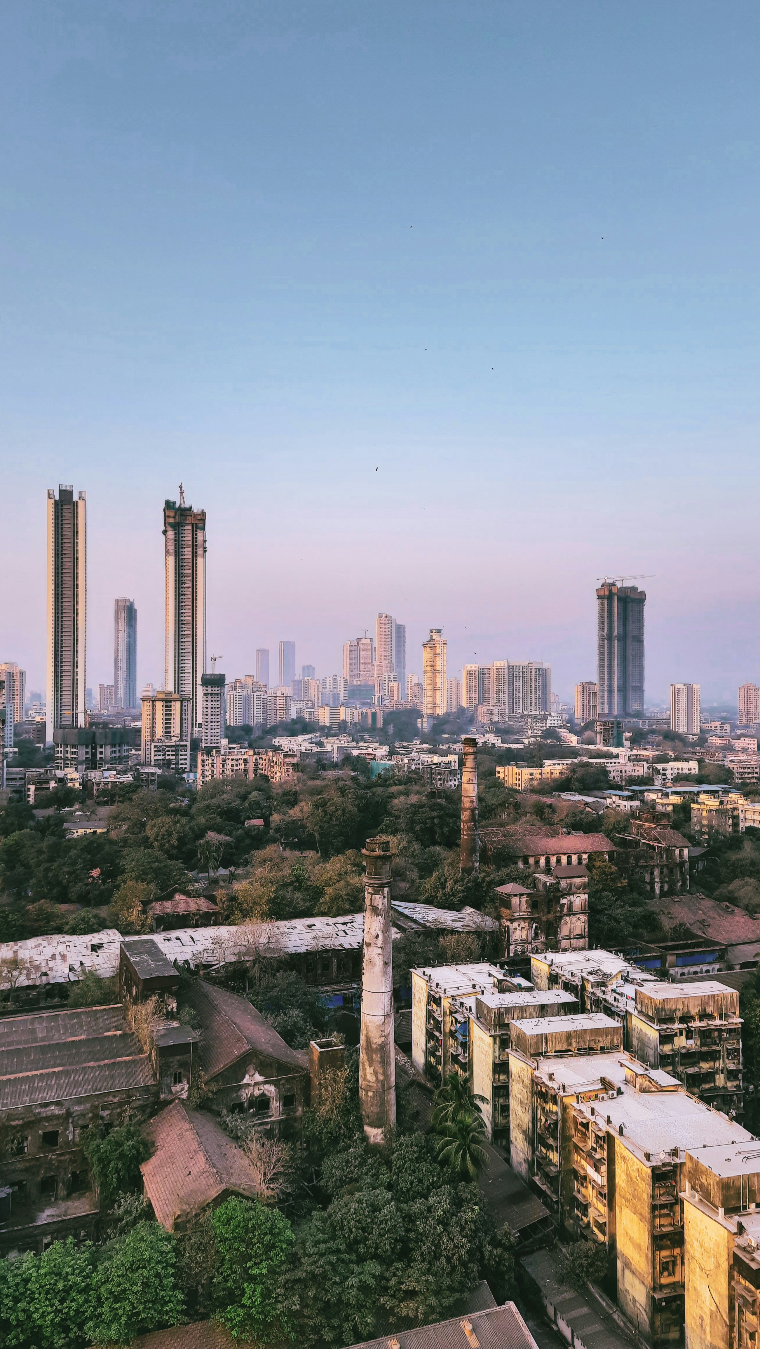 A panoramic view of a bustling cityscape showcasing a blend of modern skyscrapers and historic industrial buildings. The scene captures the essence of urban transformation.