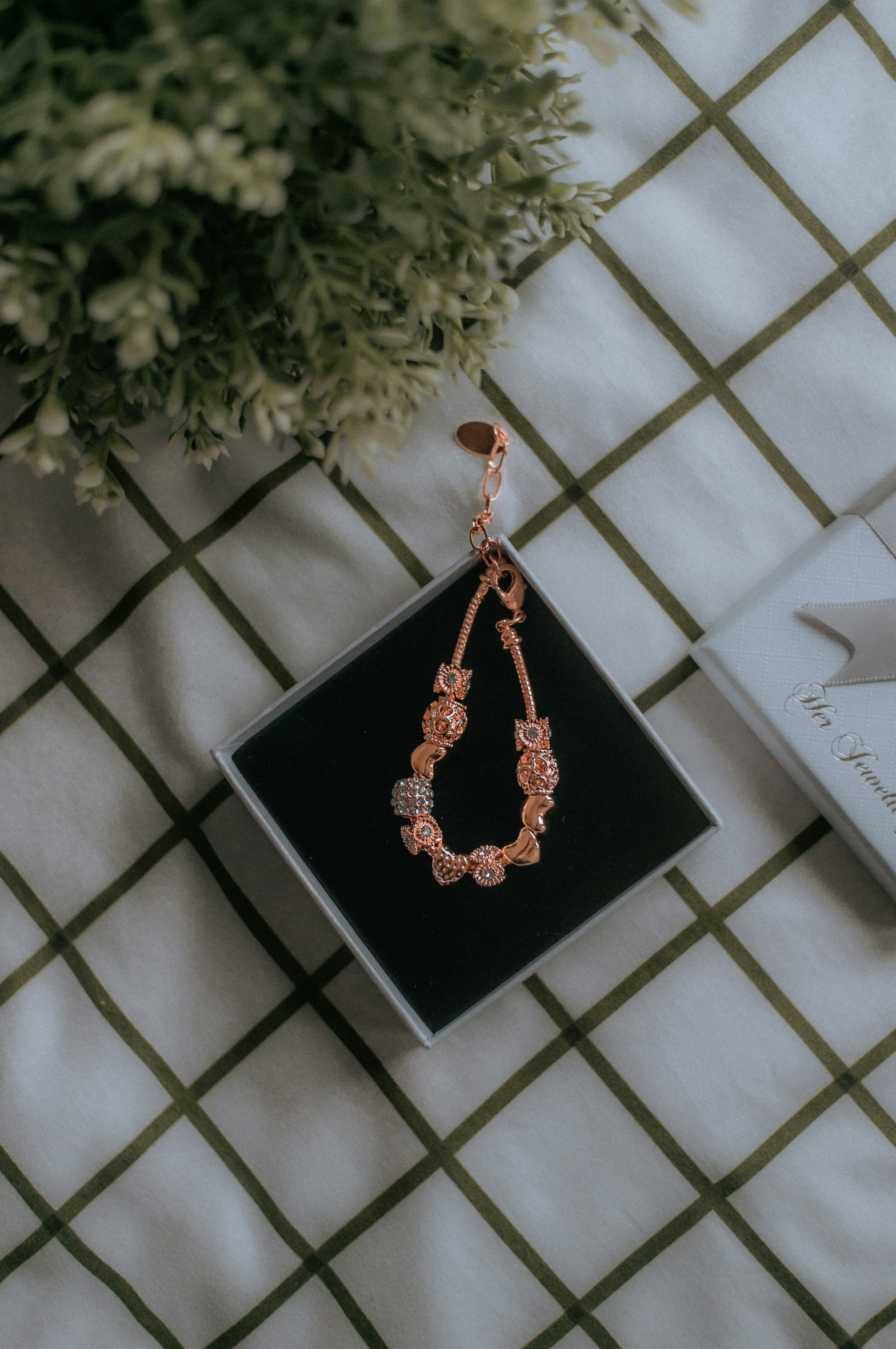 Delicate rose gold bracelet adorned with sparkling gems resting in a black box on a checkered fabric background.