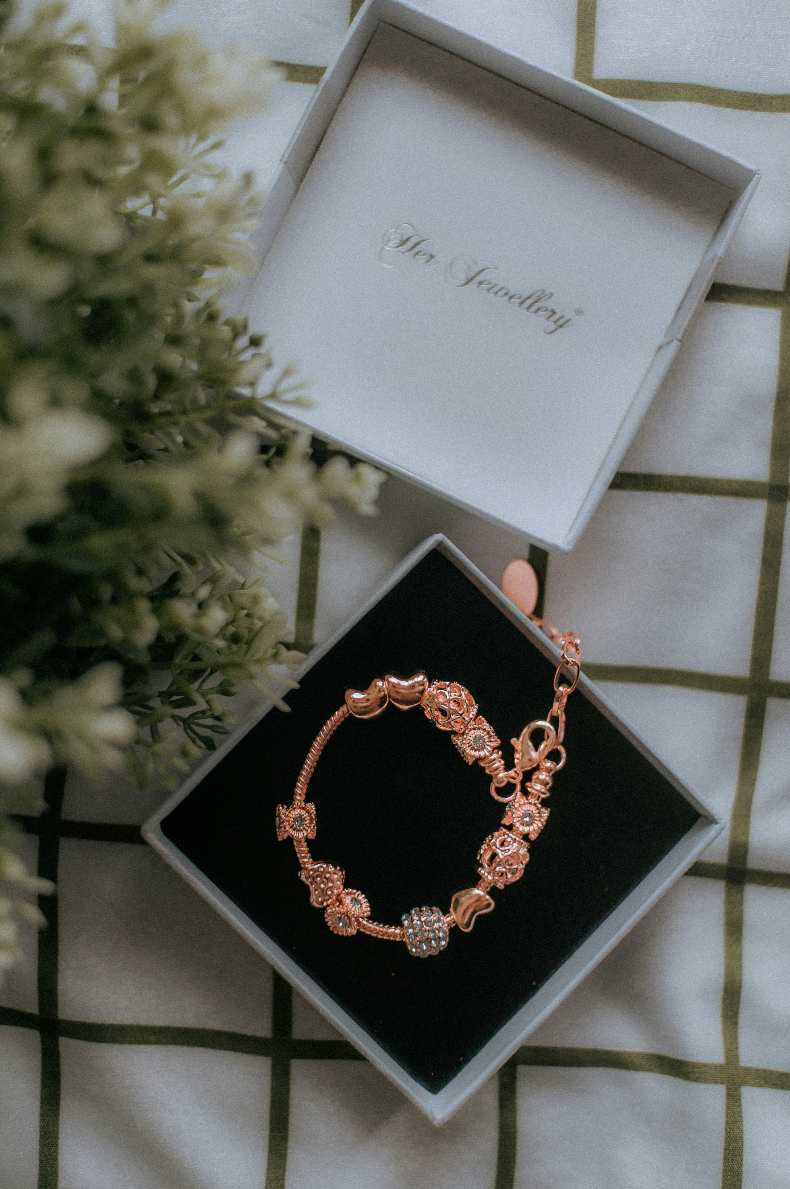 Delicate rose gold bracelet displayed in a black velvet box, surrounded by soft greenery. The jewelry box is partially open, revealing its elegant contents.