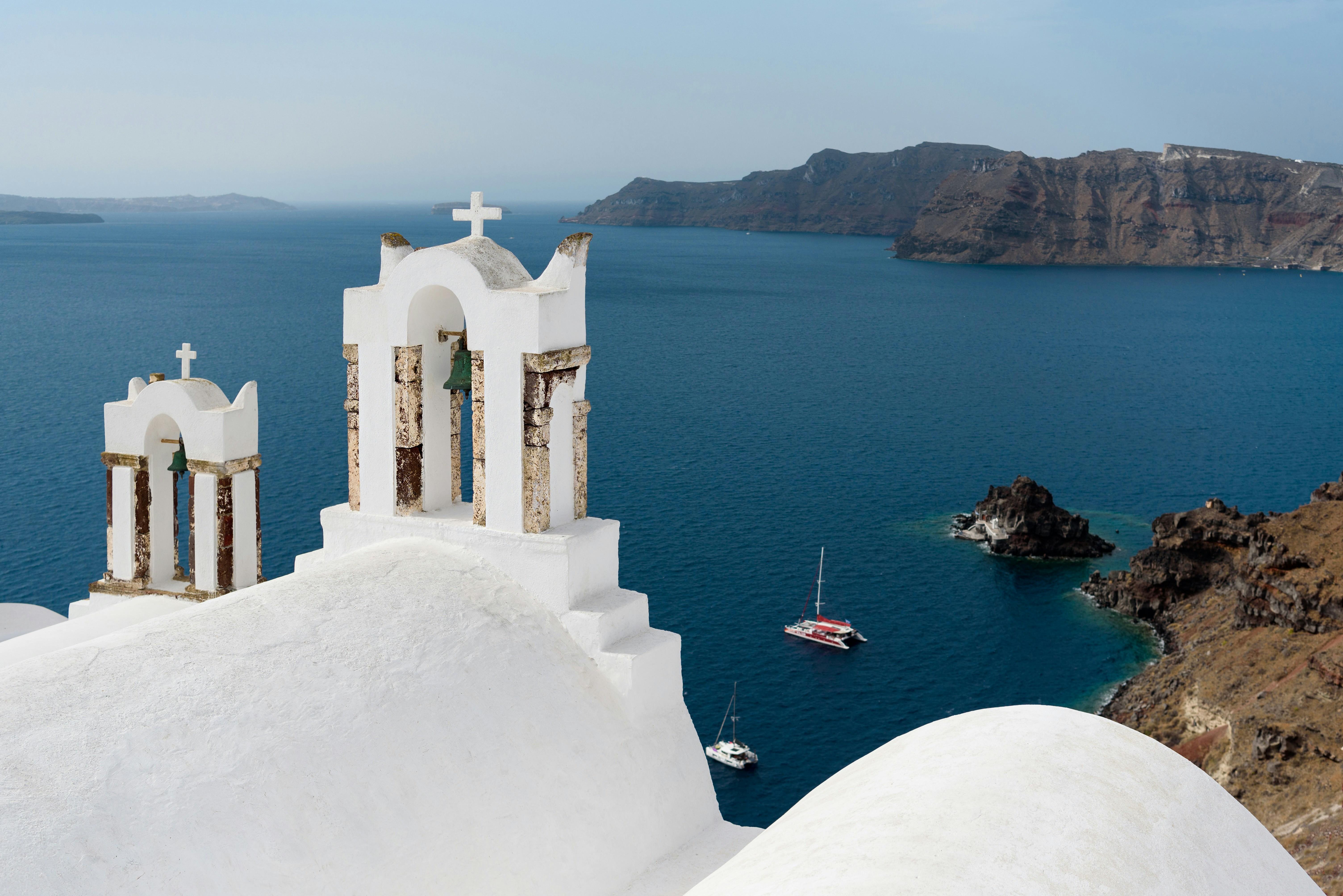 Whitewashed church with bell towers overlooking the azure sea and rugged coastline.