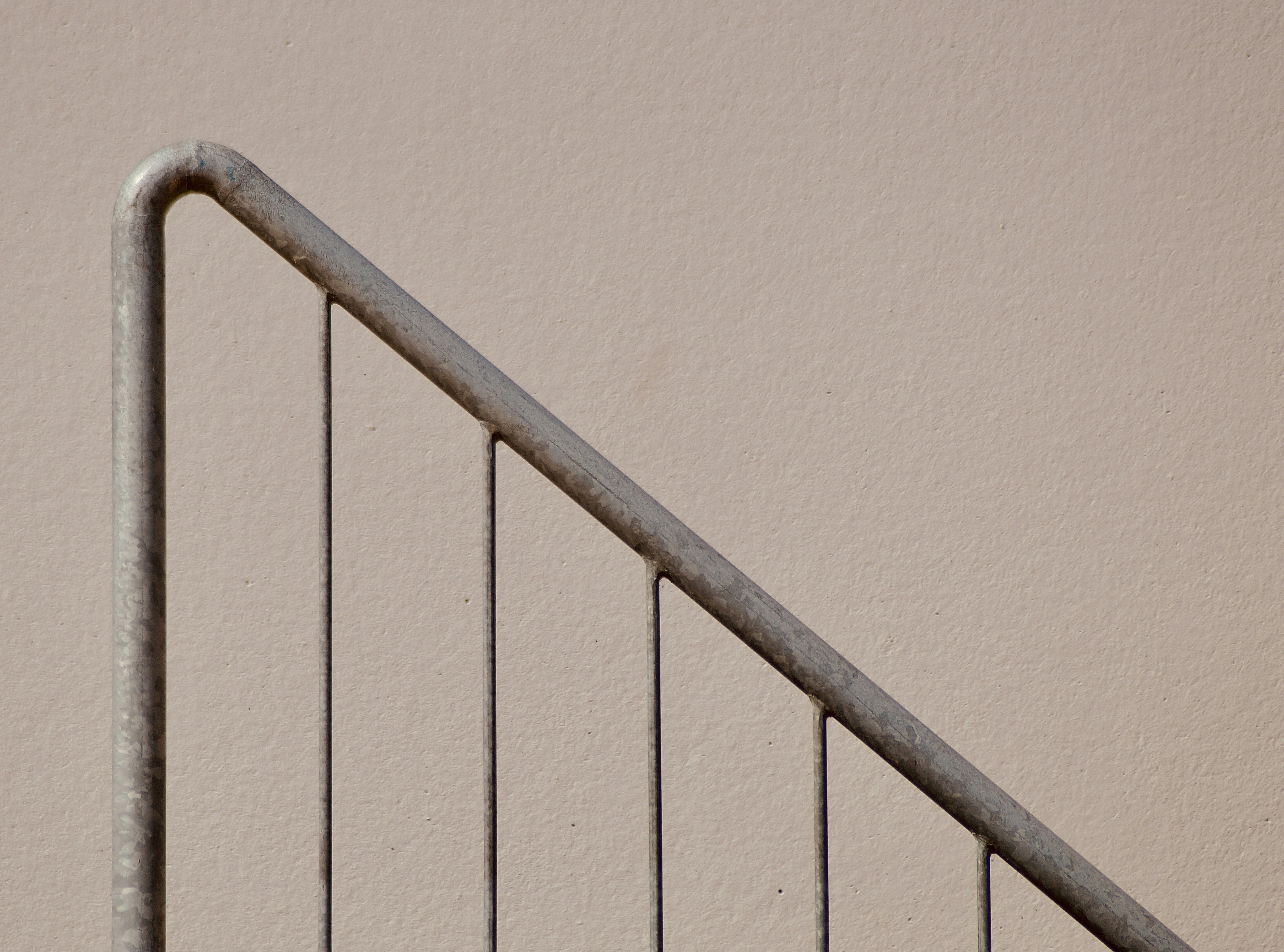 Metal railing ascending against a smooth, muted wall, showcasing a blend of industrial and minimalist aesthetics.