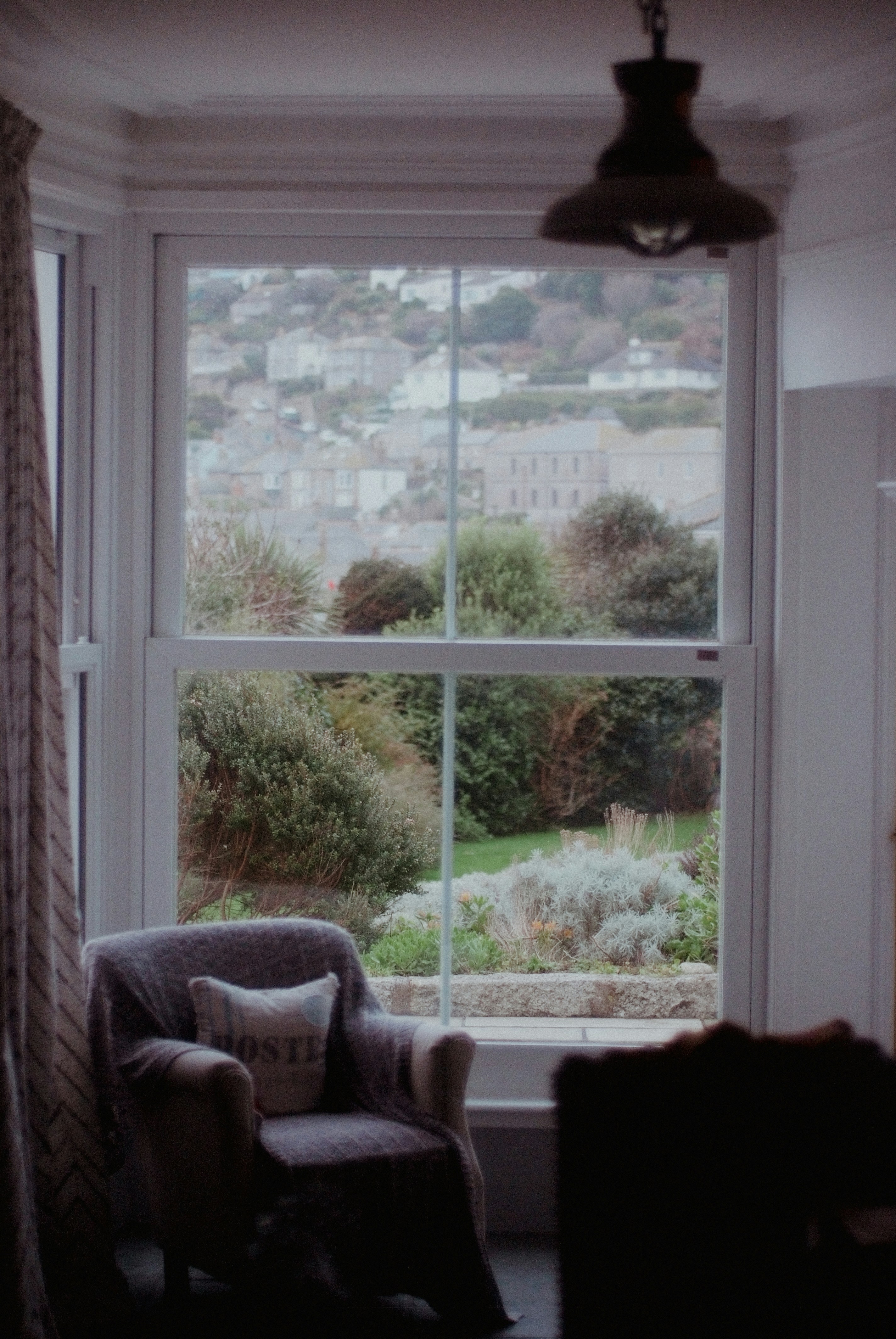 Charming interior scene featuring a cozy armchair beside a window framing a lush garden view and distant hills.
