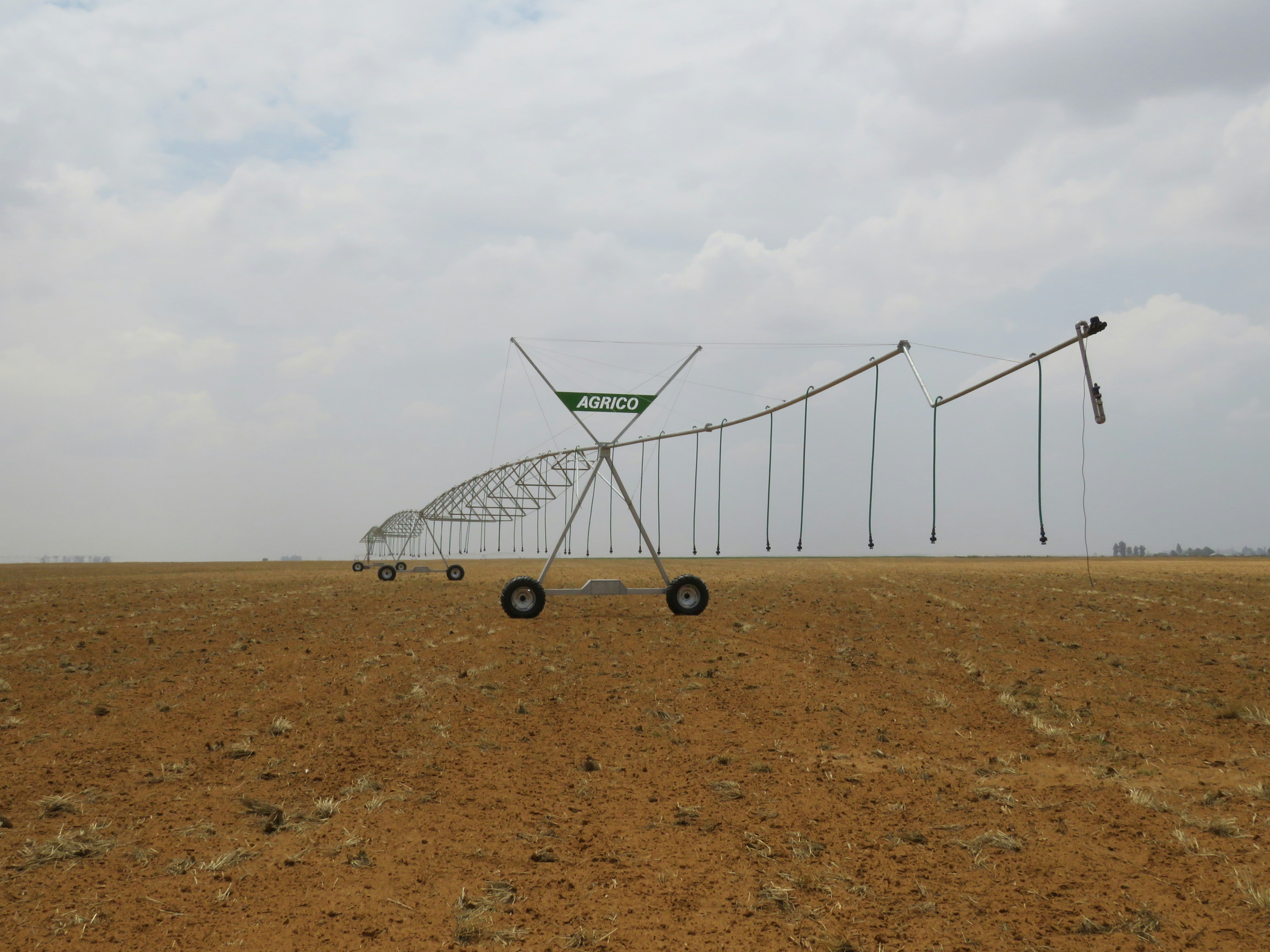 A large irrigation system stands in a vast, arid field under a cloudy sky, showcasing modern agricultural technology.