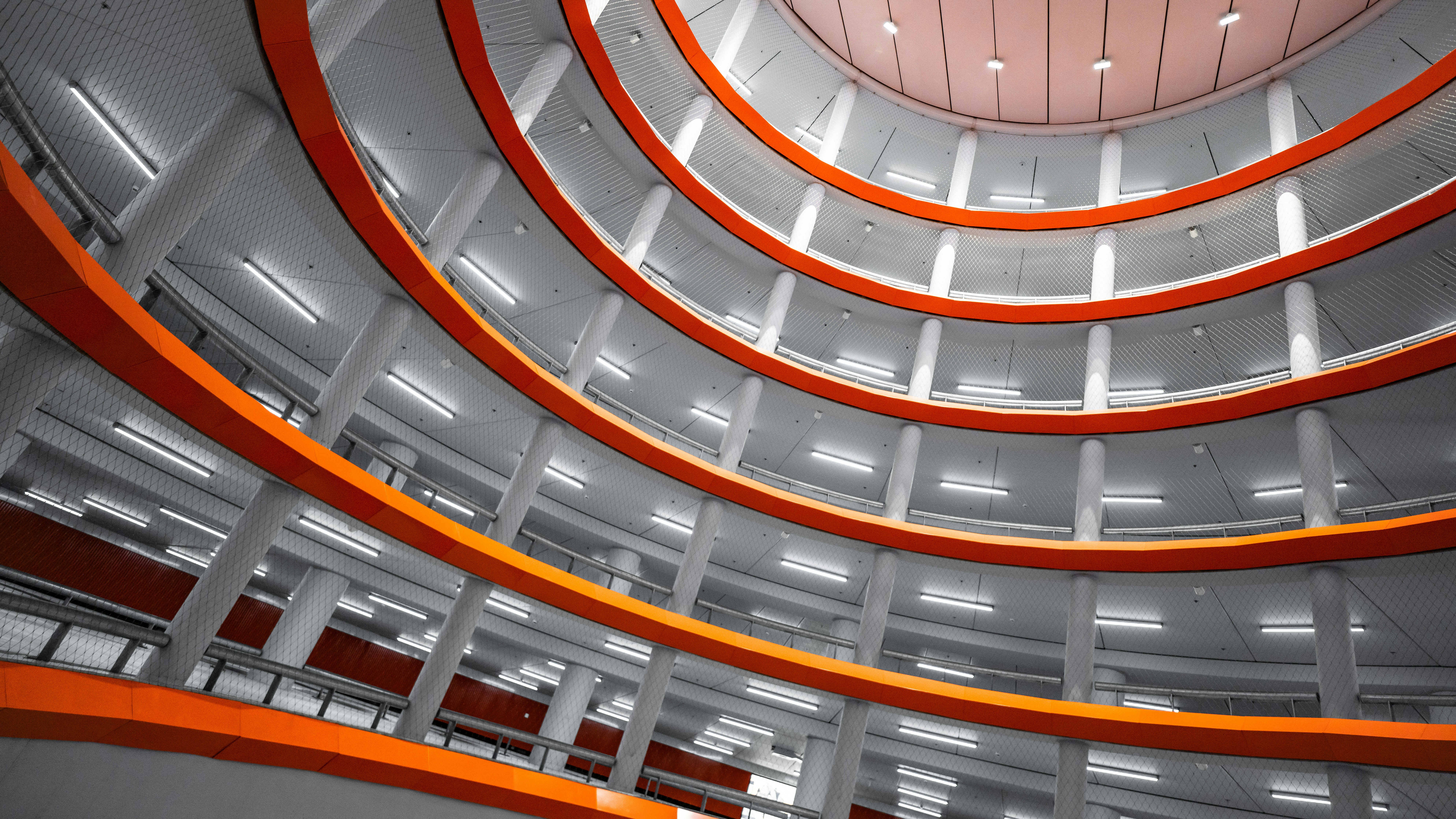 Interior view of a multi-level parking garage with orange accents and concentric circular design.