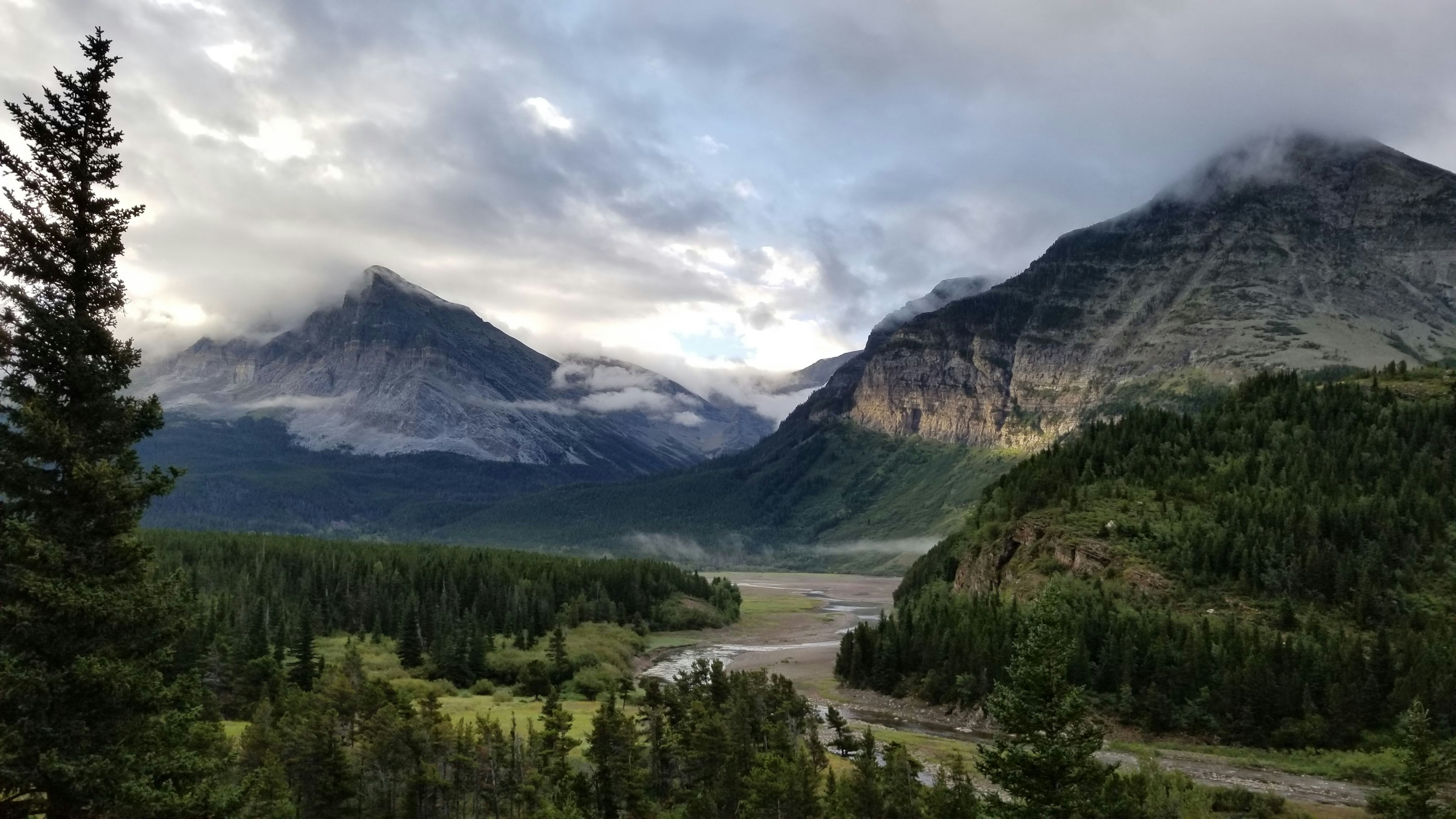 Winding River Through a Conifer-Valley Beneath Cloud-Wreathed Peaks