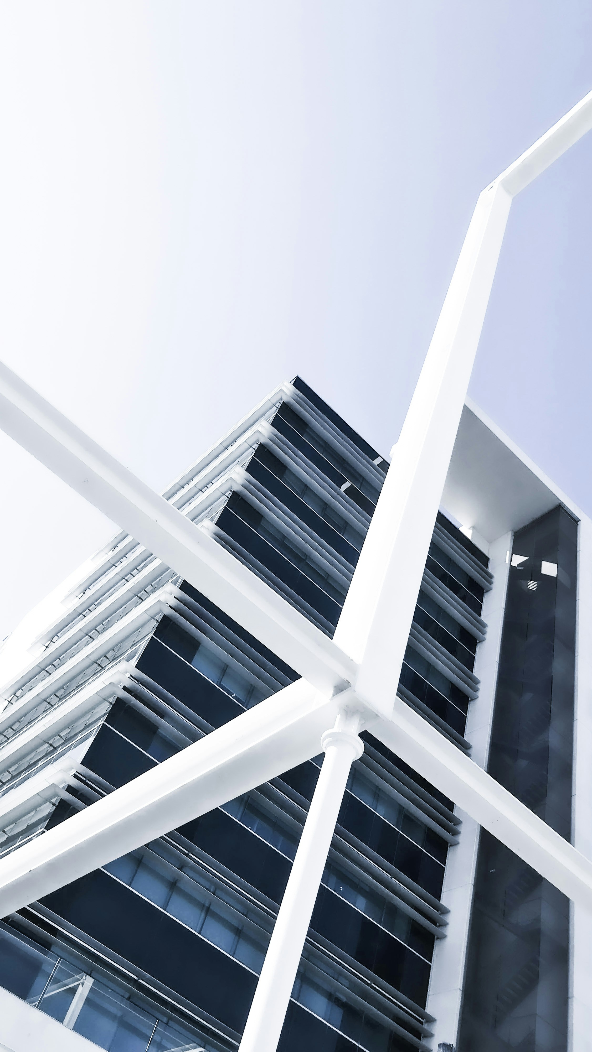 A sleek modern building framed by intersecting white beams, showcasing a blend of lines and structures. The image emphasizes architectural design and spatial dynamics.