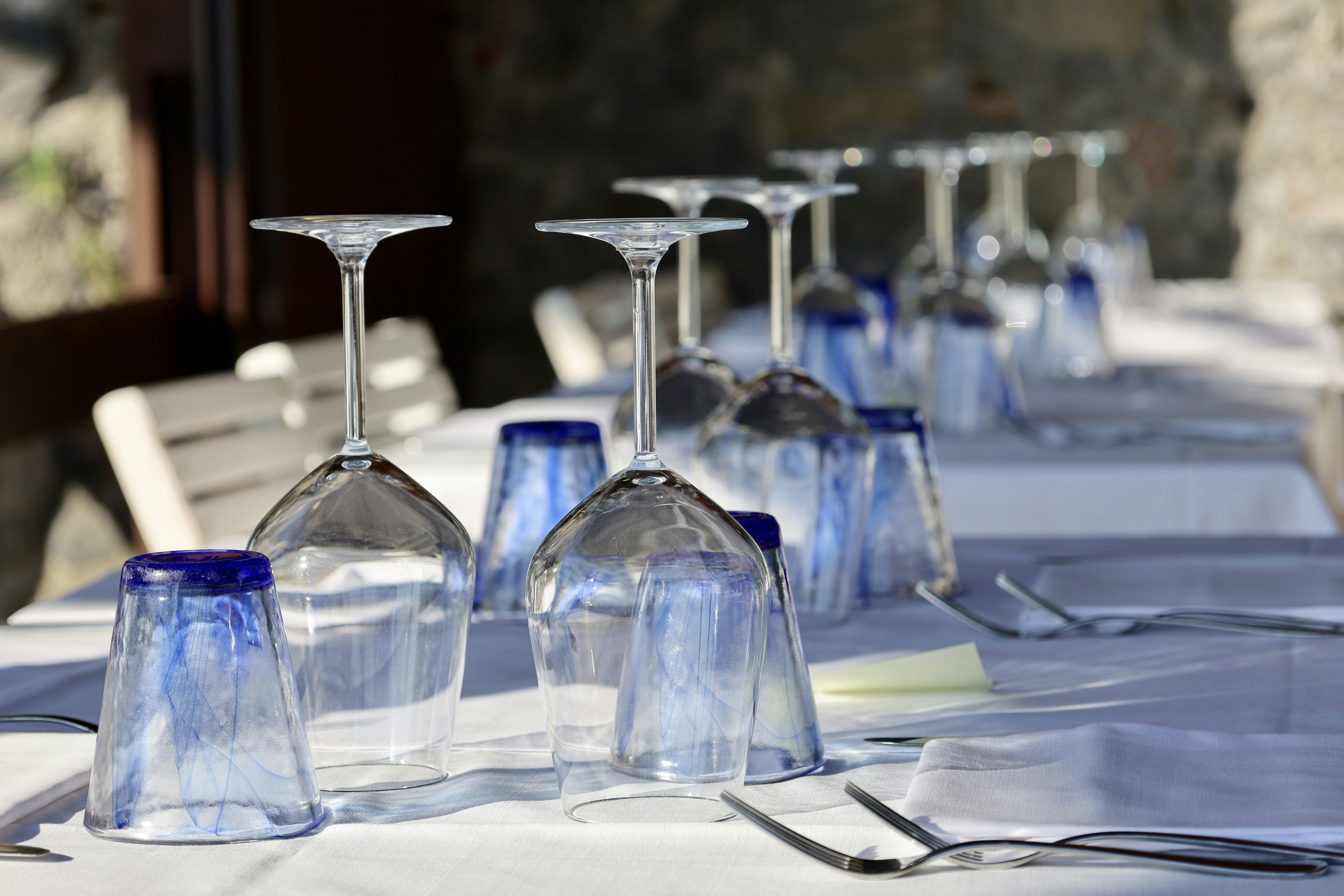 Table elegantly set with crystal wine glasses and blue-tinted tumblers, reflecting natural light. The arrangement hints at an inviting dining experience.
