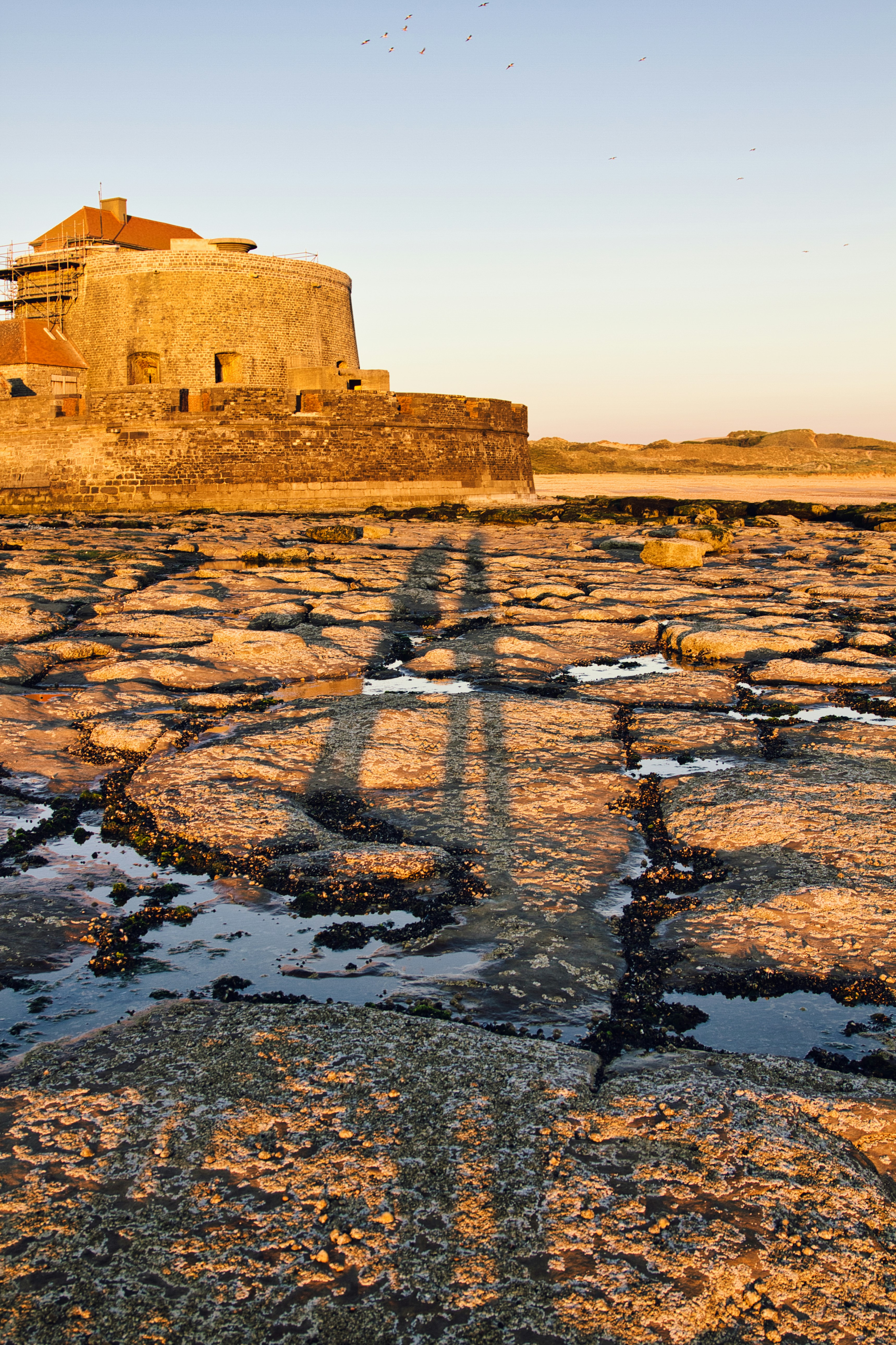 Golden Shadows on Cracked Flats Head Toward a Coastal Fort at Sunset