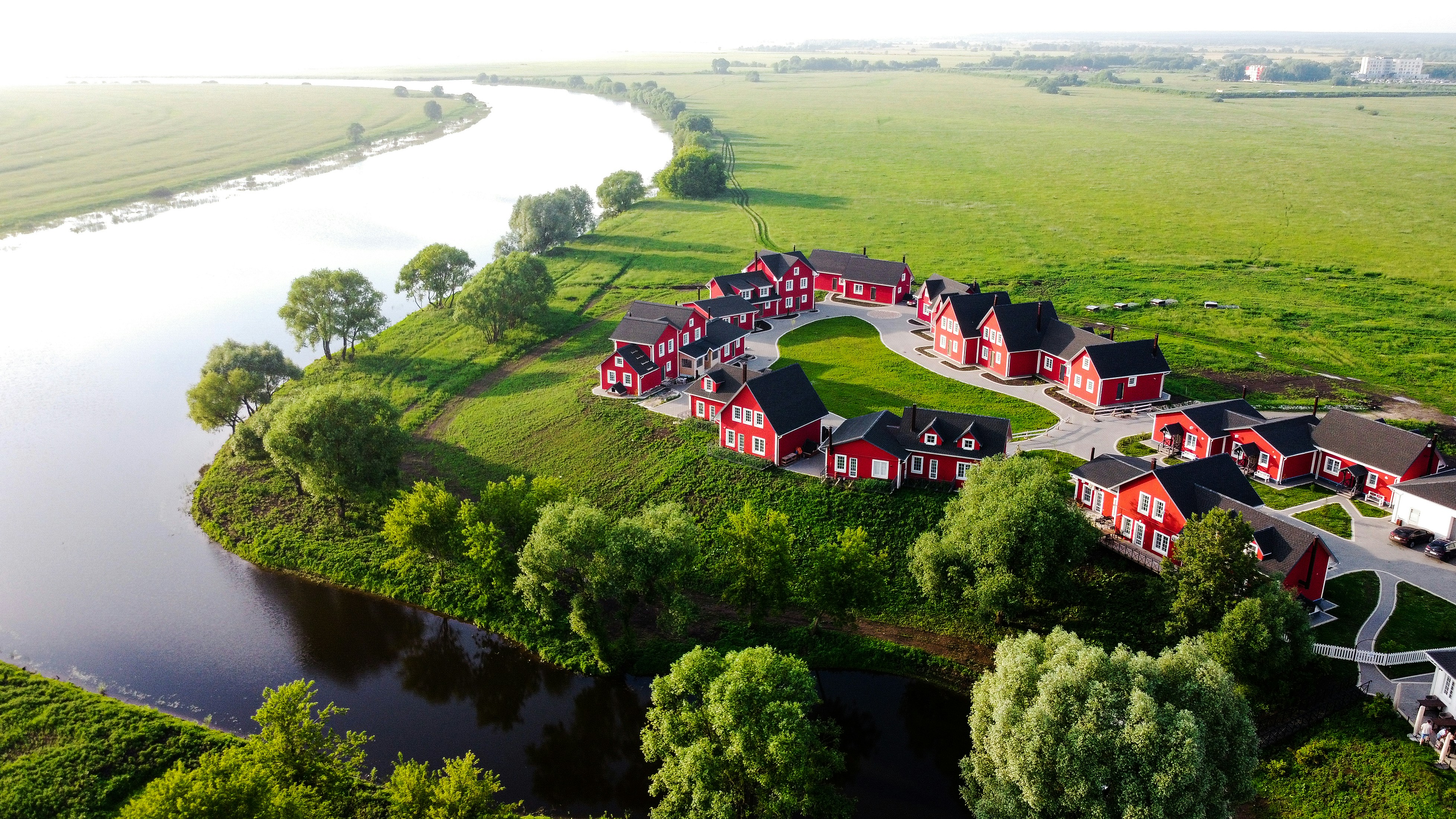 Aerial view of quaint red-roofed village nestled by a winding river in lush green fields.
