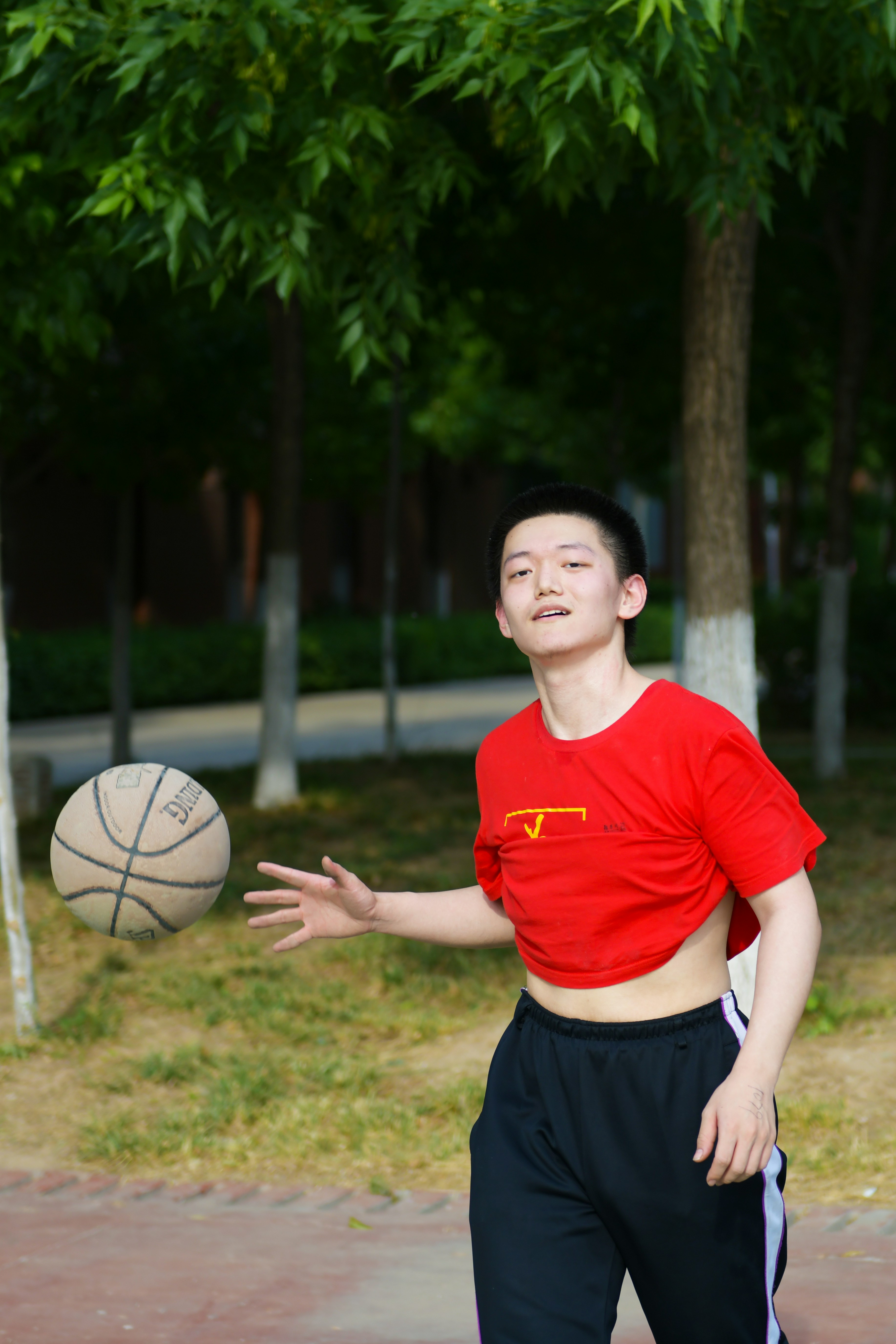 Young athlete in a red shirt skillfully tossing a basketball while surrounded by greenery.